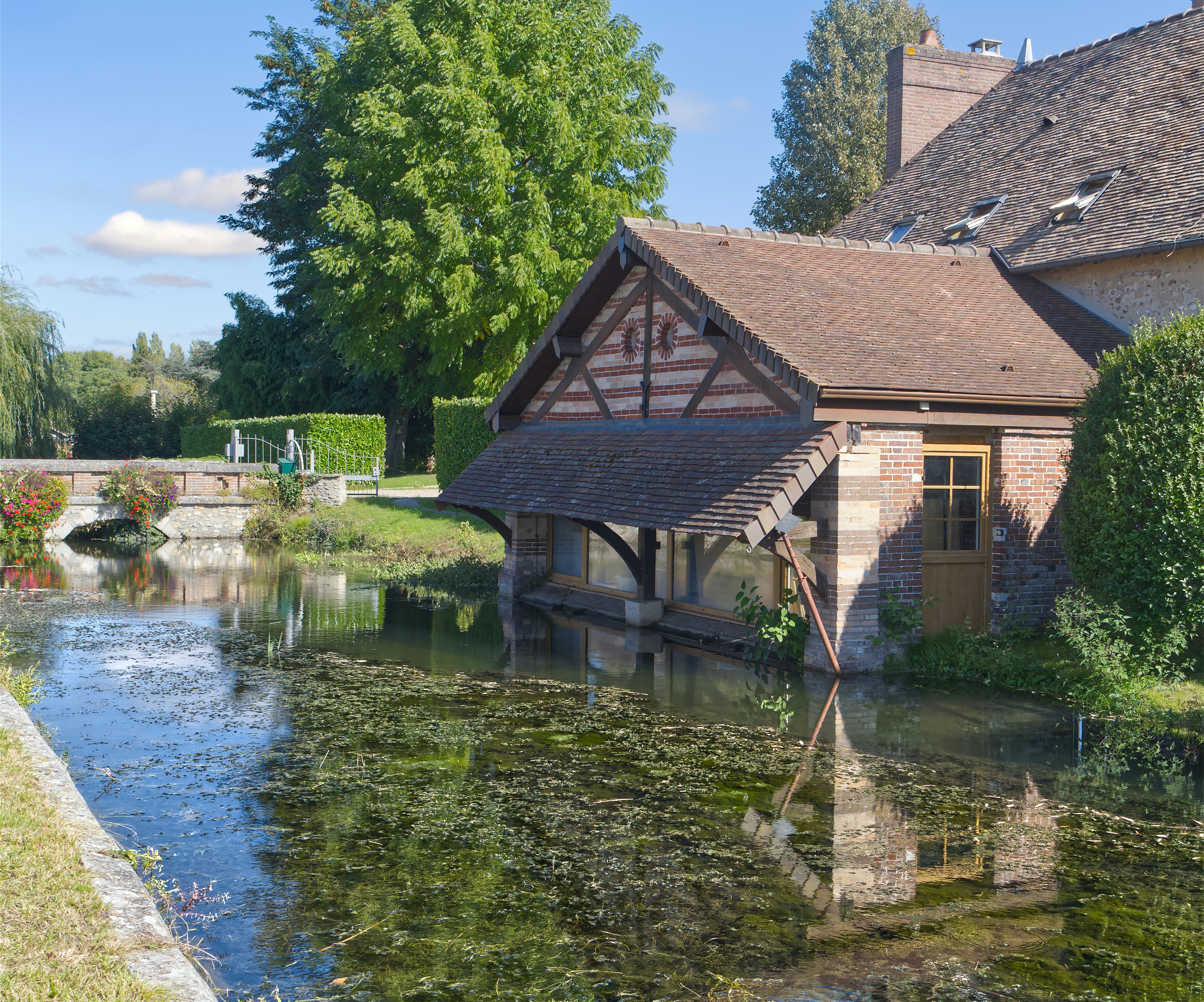 Sur les méandres apaisants de l’Eure, où la rivière dessine un réseau de bras sinueux, se niche le village de Croisy-sur-Eure, un des joyaux de la vallée normande. Au cœur de ce paysage préservé, le lavoir de la ferme du château se dresse comme un témoin silencieux de l’histoire locale. Érigé le 18 novembre 1873, il incarne l’élégance et la fonctionnalité des constructions du XIXe siècle, tout en restant le plus emblématique des trois lavoirs de la commune. Autrefois lieu de labeur et de rencontres pour les lavandières, il est aujourd’hui une invitation à la contemplation, où la pierre et l’eau s’unissent pour rappeler la vie villageoise d’autrefois.