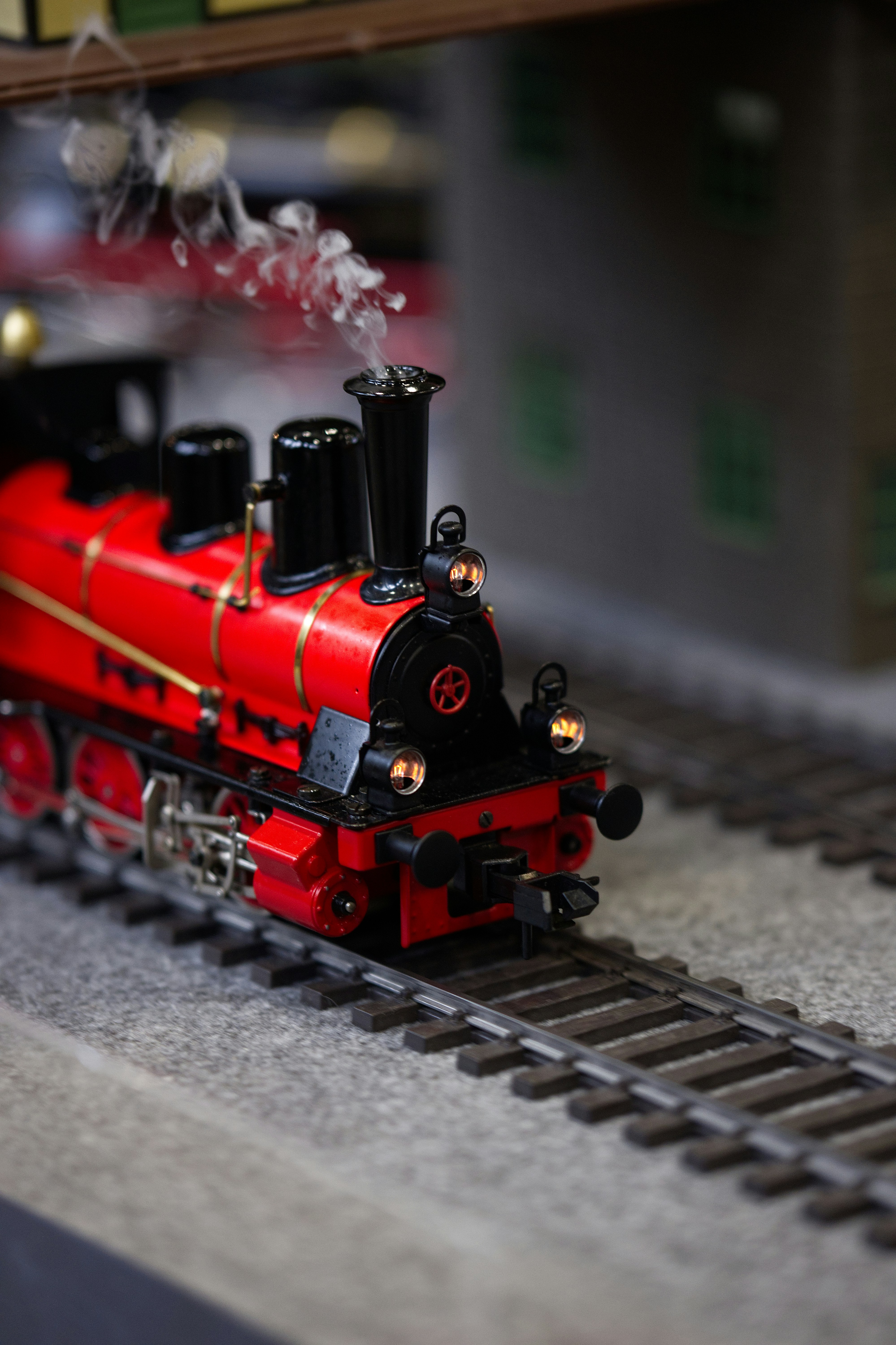 Detailed model steam locomotive emitting smoke, set against a backdrop of miniature buildings and tracks.