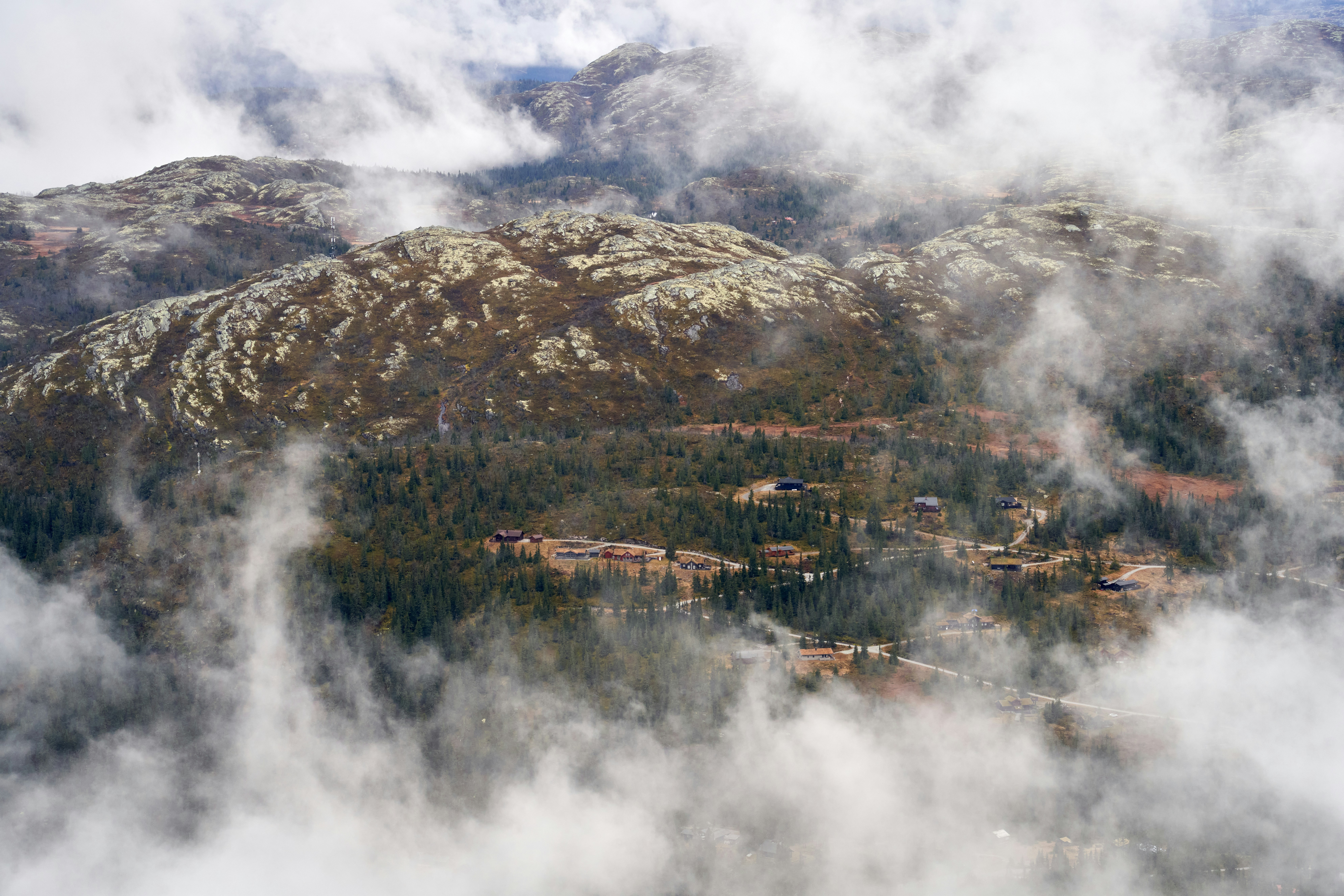 Aerial view of a secluded settlement nestled among rolling hills, partially obscured by swirling clouds and mist.