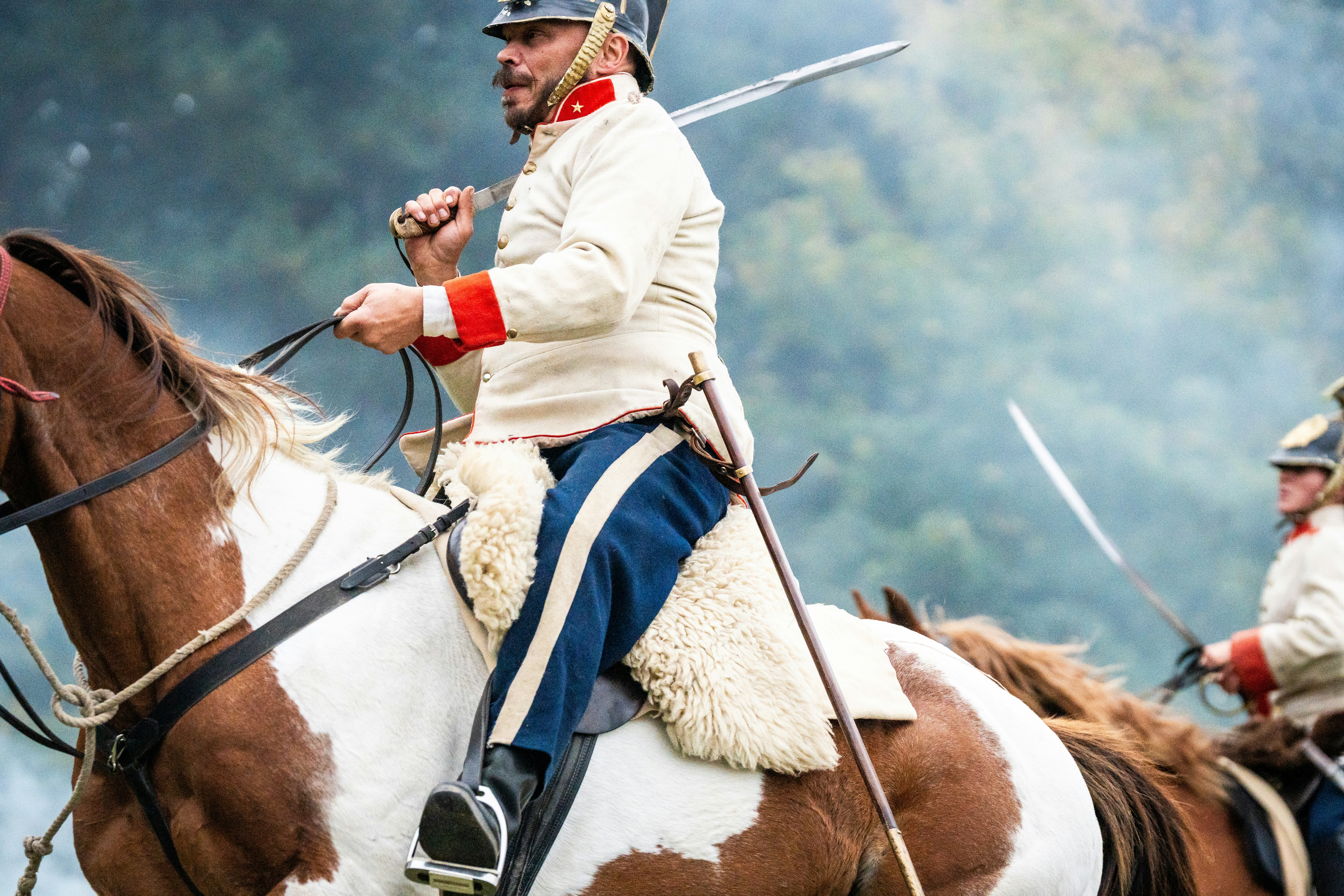 Historical reenactor on horseback brandishing a sword, dressed in period military attire, with a misty forest backdrop.