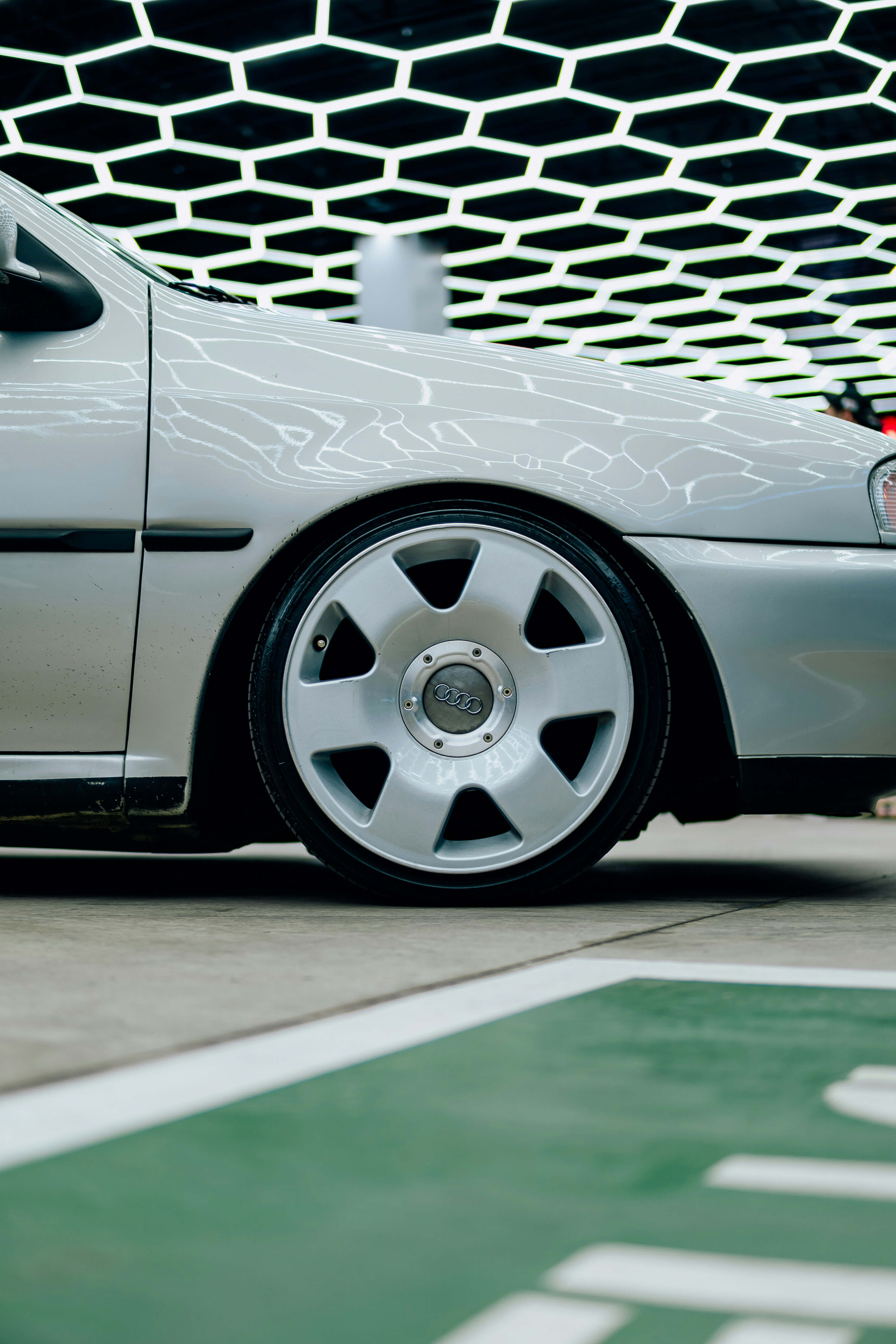 Hex-grid Reflections: Close-Up of a Silver Wheel Beneath a Geometric Parking Ceiling