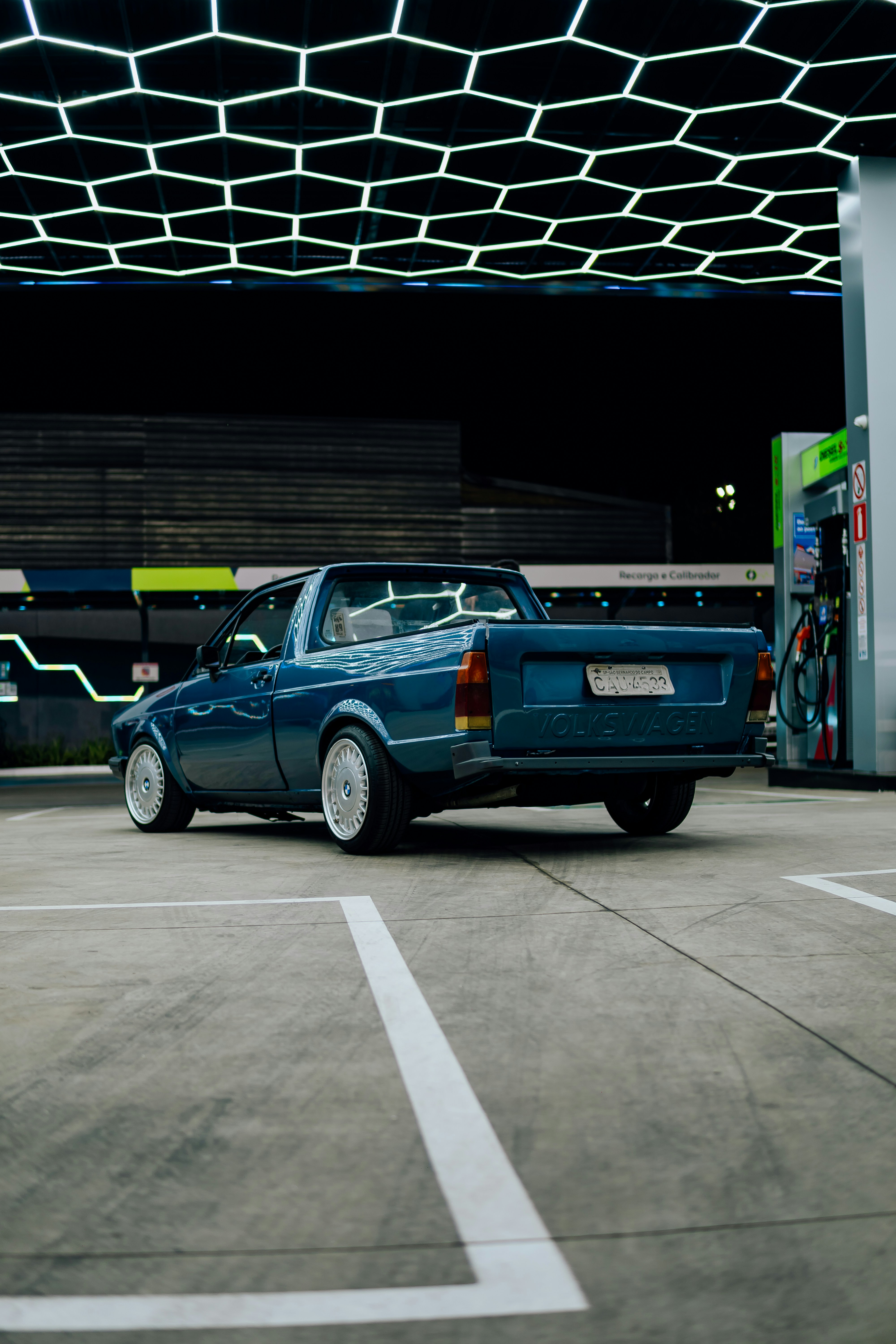 Midnight-Blue Sedan Under a Neon Hex Canopy at a Quiet Gas Stop