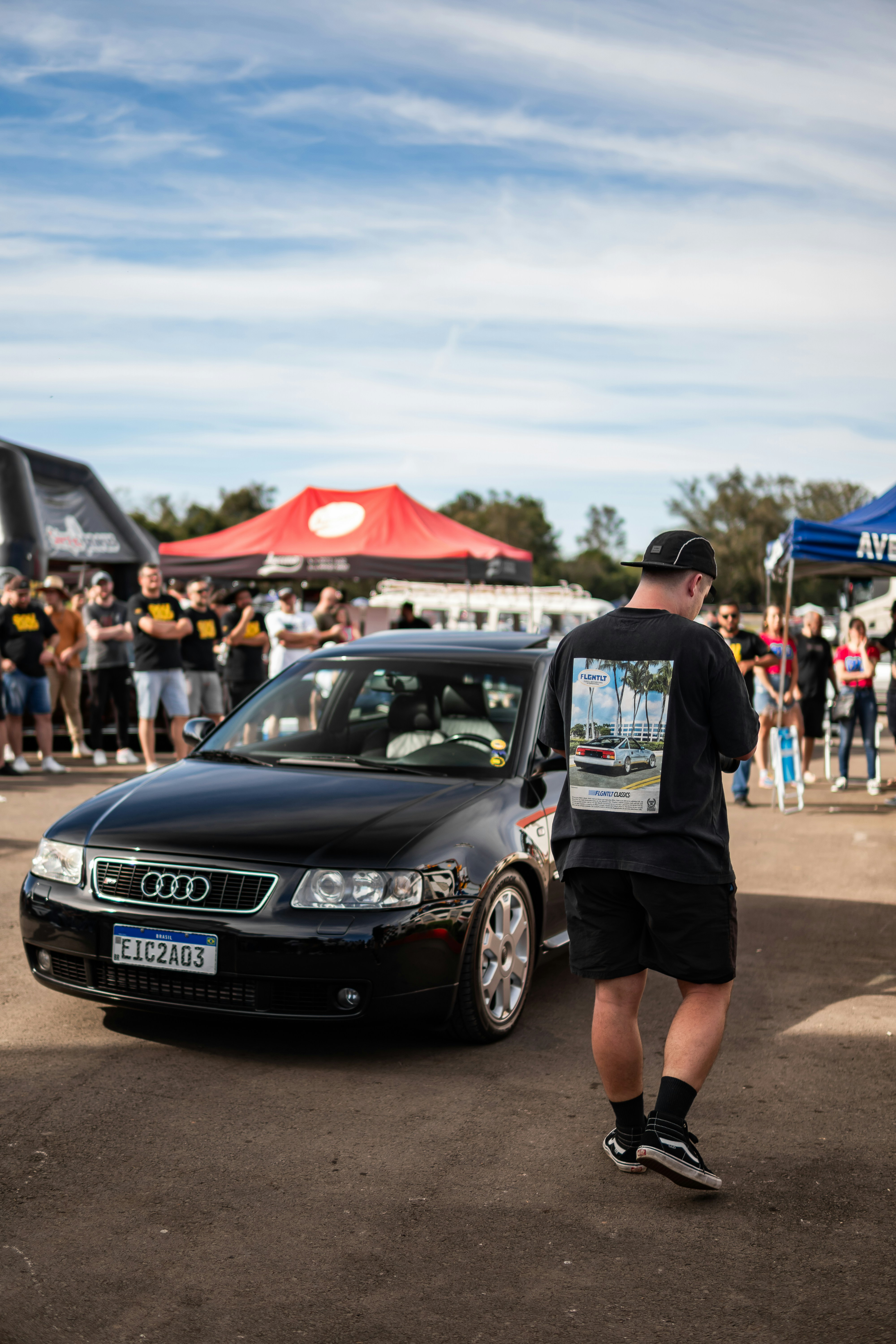 Midday Spotlight on a Black Audi: Wheels, Crowd, and Red Canopies