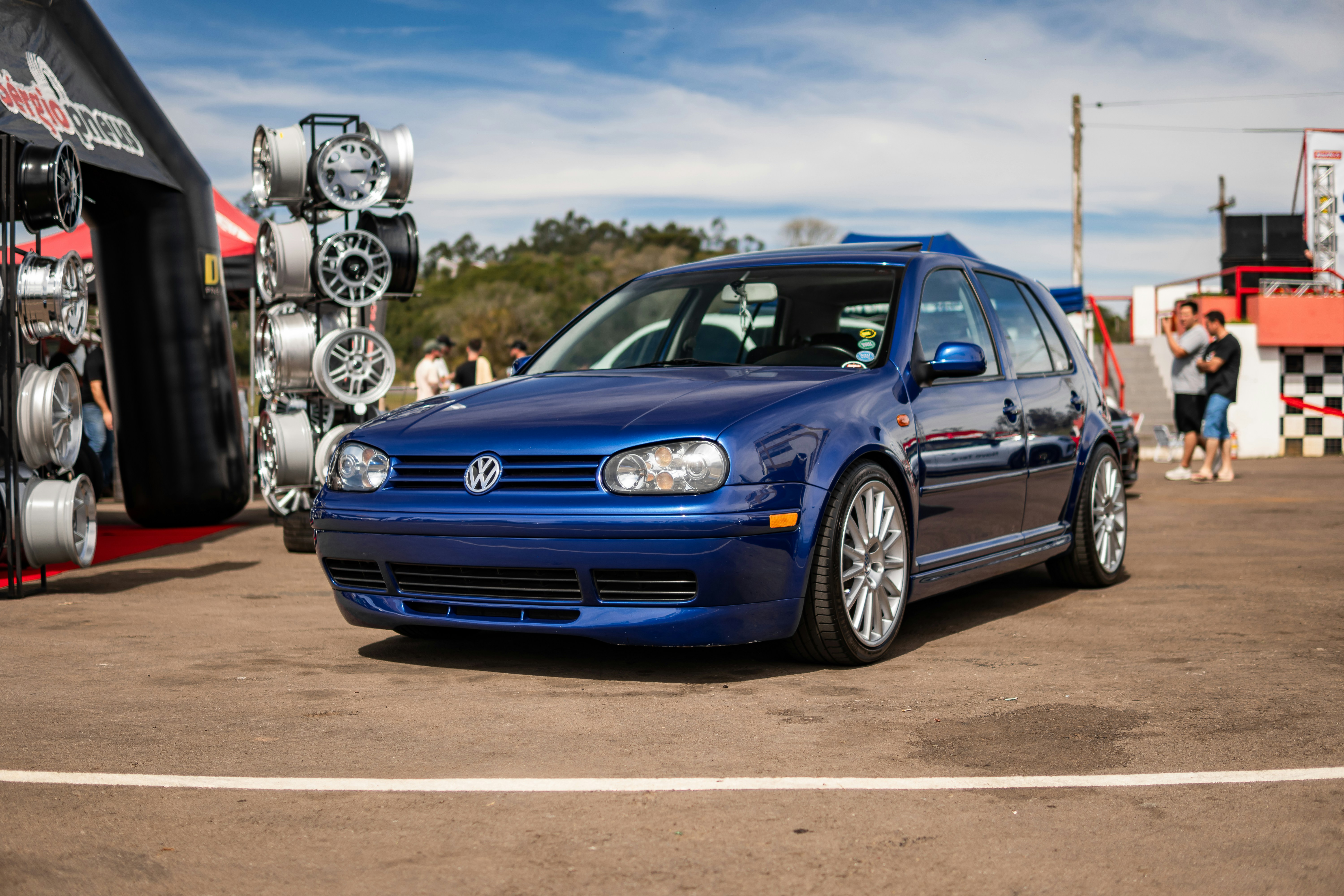 Azure VW Golf Mk4 Under the Wheel Display at a Sunlit Car Show