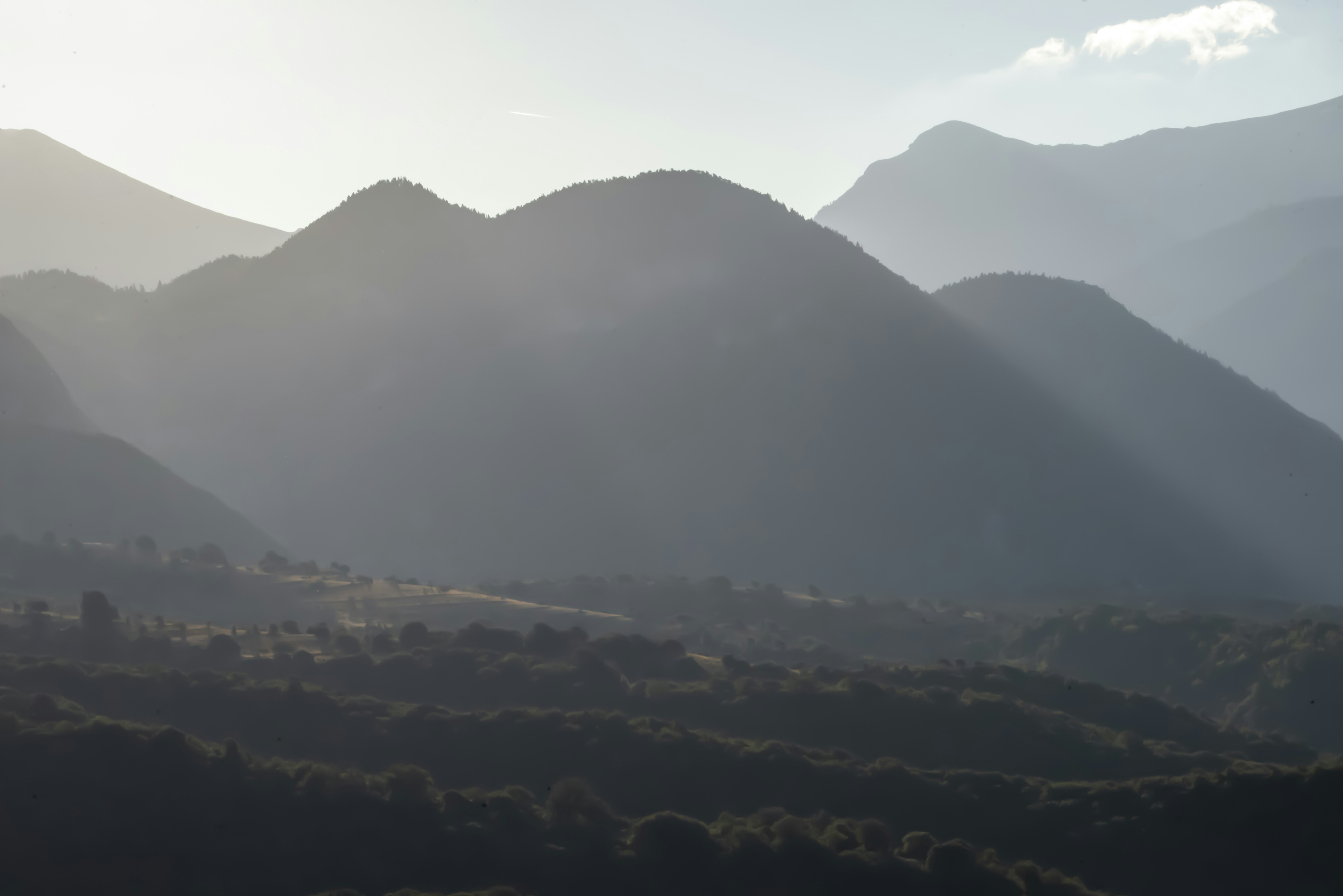 Layered mountain silhouettes shrouded in soft morning light, creating a serene landscape. The image captures the essence of tranquility in nature.