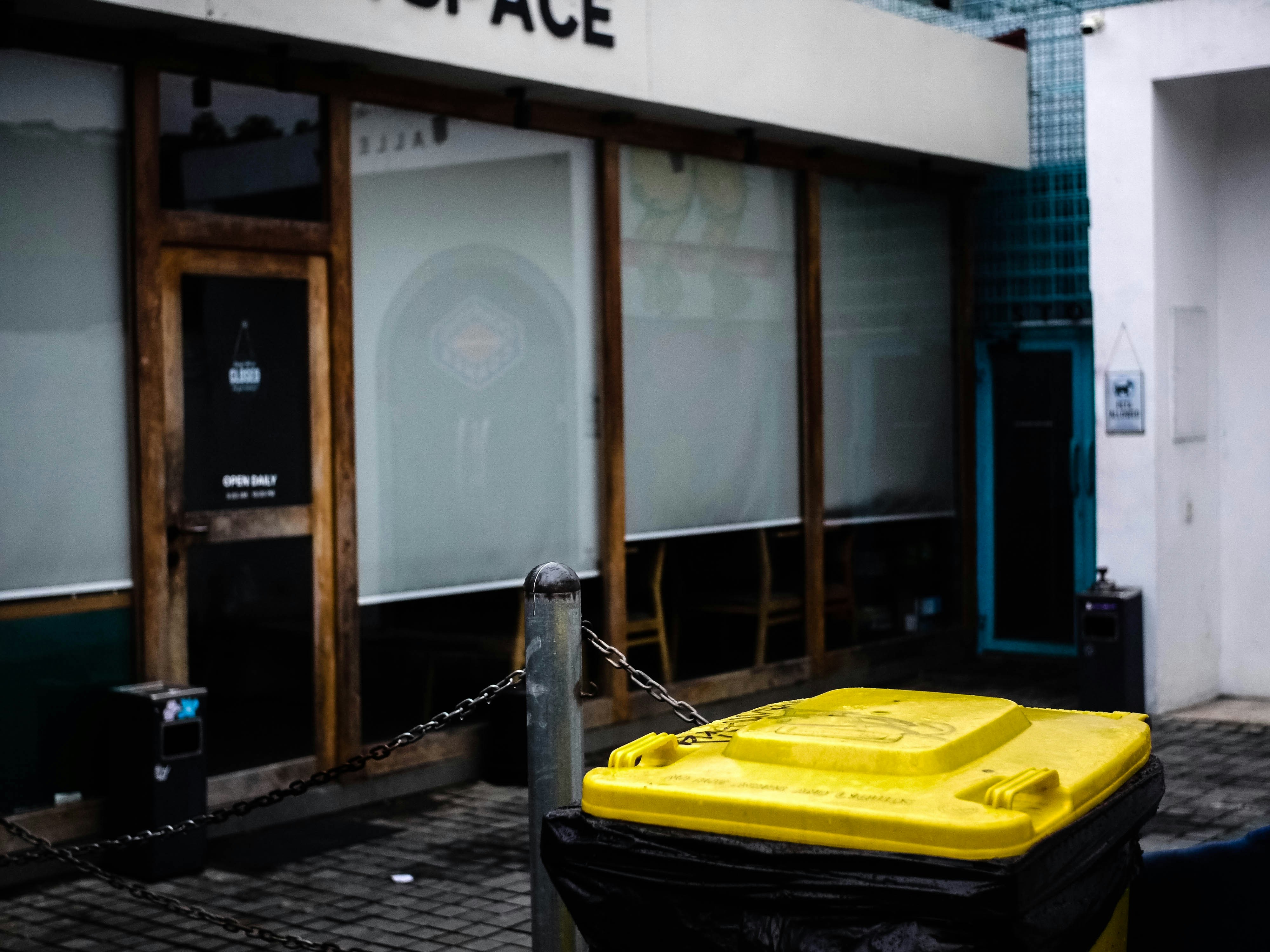 Urban Contrast: The Yellow Bin Framed by Glass and Chains