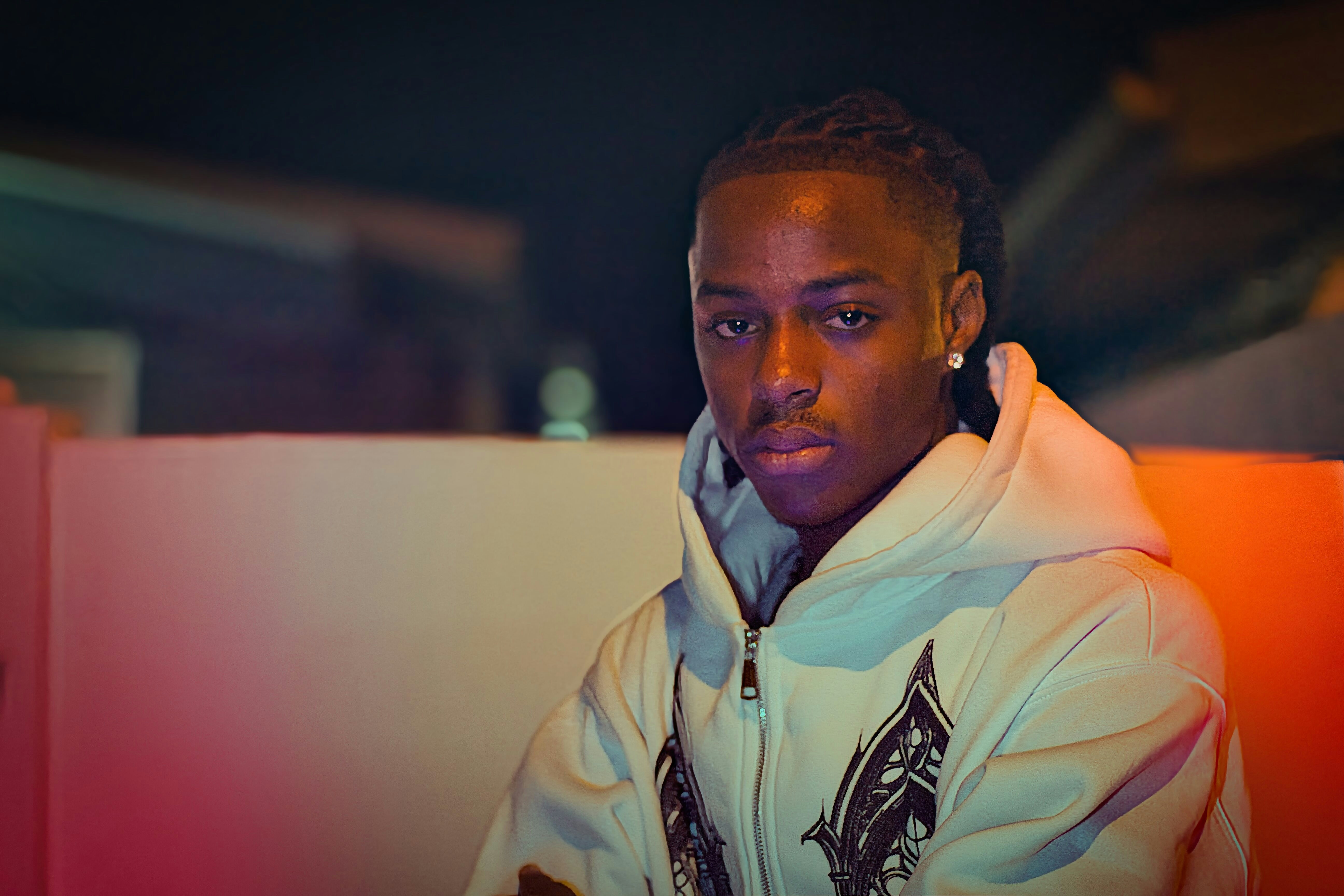 Young man in a stylish hoodie poses against a softly lit urban backdrop, capturing the essence of nightlife culture.