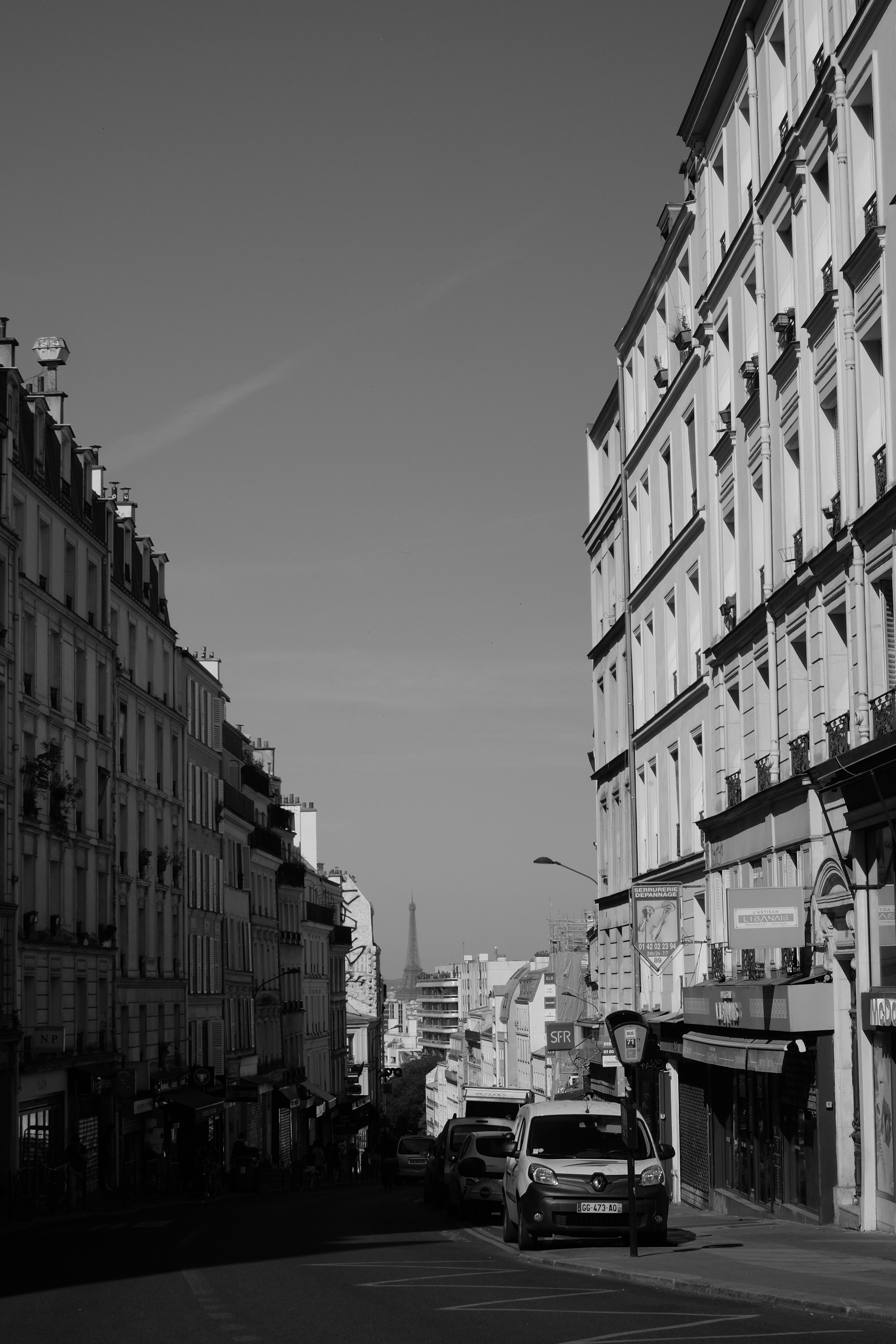 Narrow Paris street lined with classic architecture, leading to the distant silhouette of the Eiffel Tower in a monochrome setting.