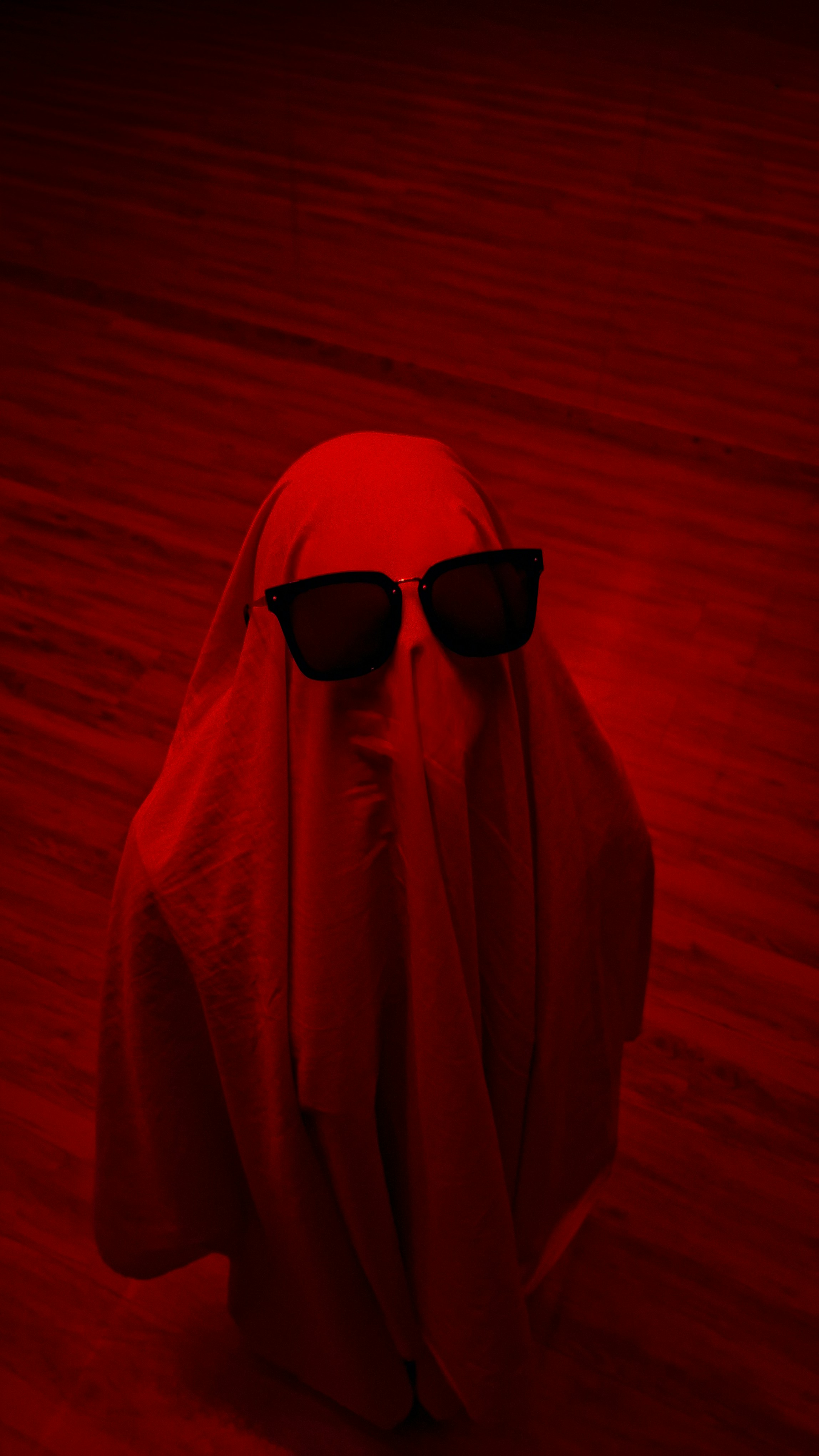 Part of a photo series — see more on my profile! A minimal conceptual photo of a ghost figure draped in red light, standing confidently with black sunglasses. The surreal contrast between fear and humor gives the image a playful yet eerie atmosphere — blending absurdism and Halloween aesthetics. Model featured gave full consent for photography and Unsplash publication. Model’s face is intentionally covered for privacy.