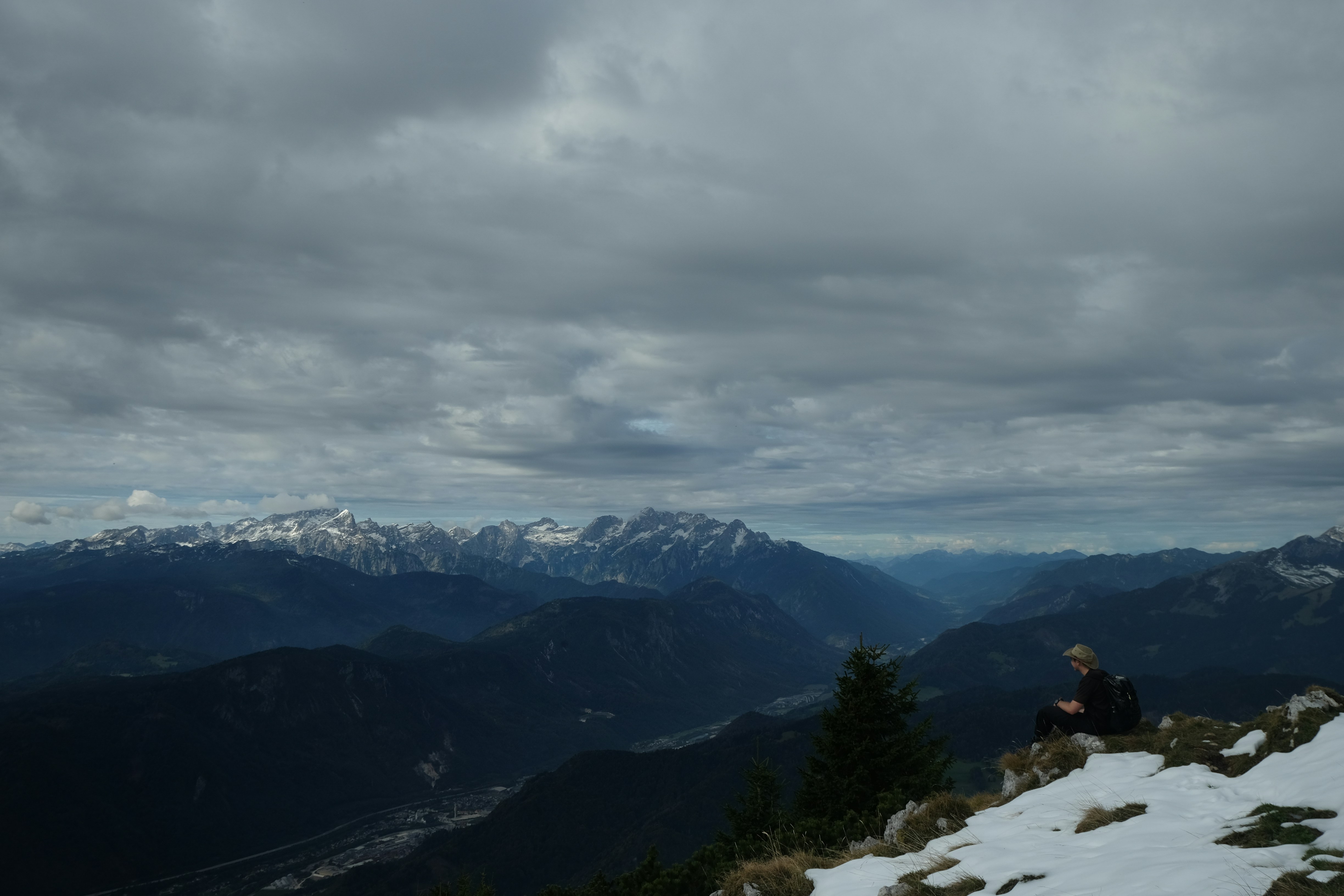 A person sits on a snowy mountain peak overlooking valley.
