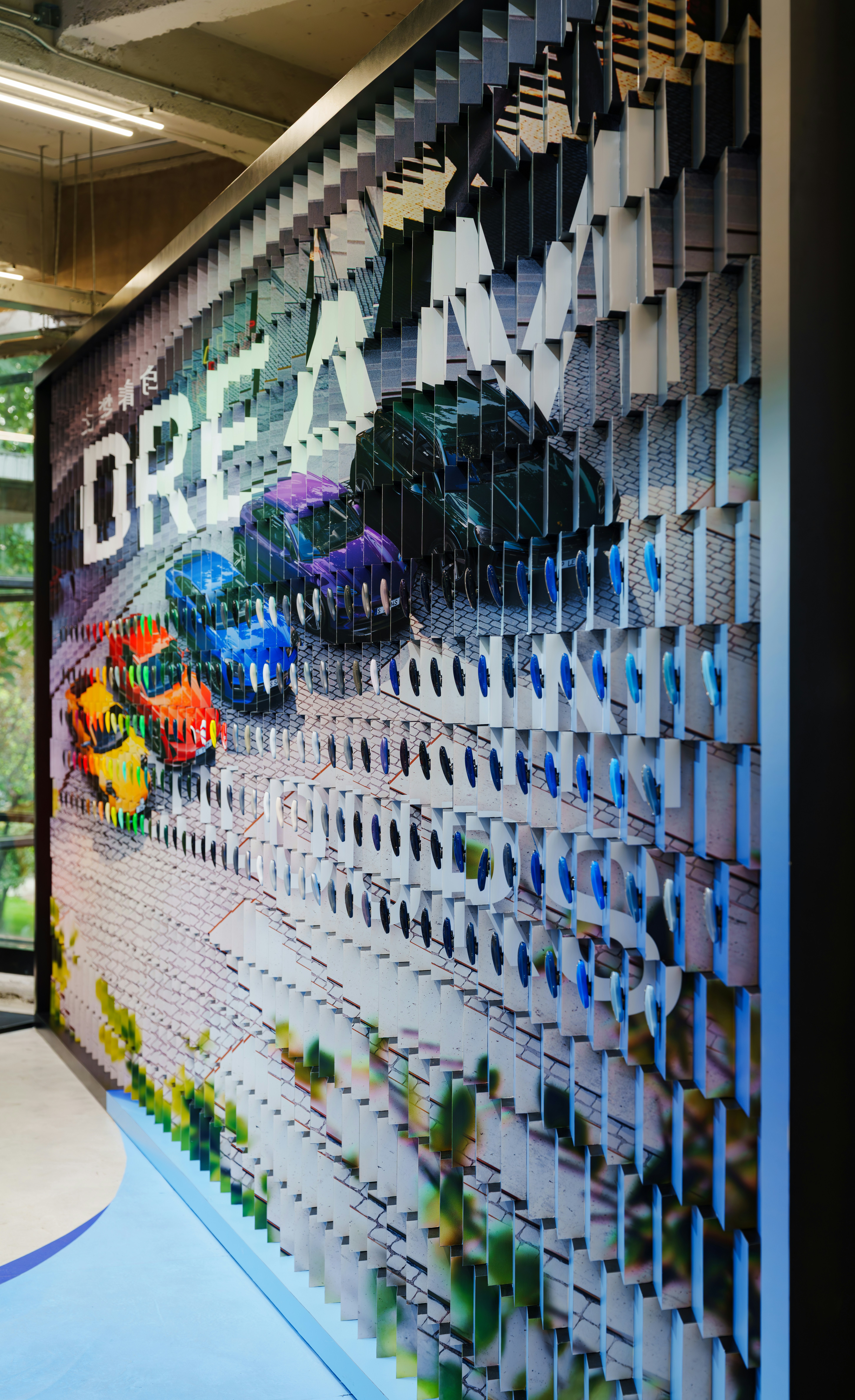 A vibrant wall installation featuring layered images of colorful cars, creating a dynamic visual experience. The artwork invites viewers to engage with the theme of aspiration and movement.