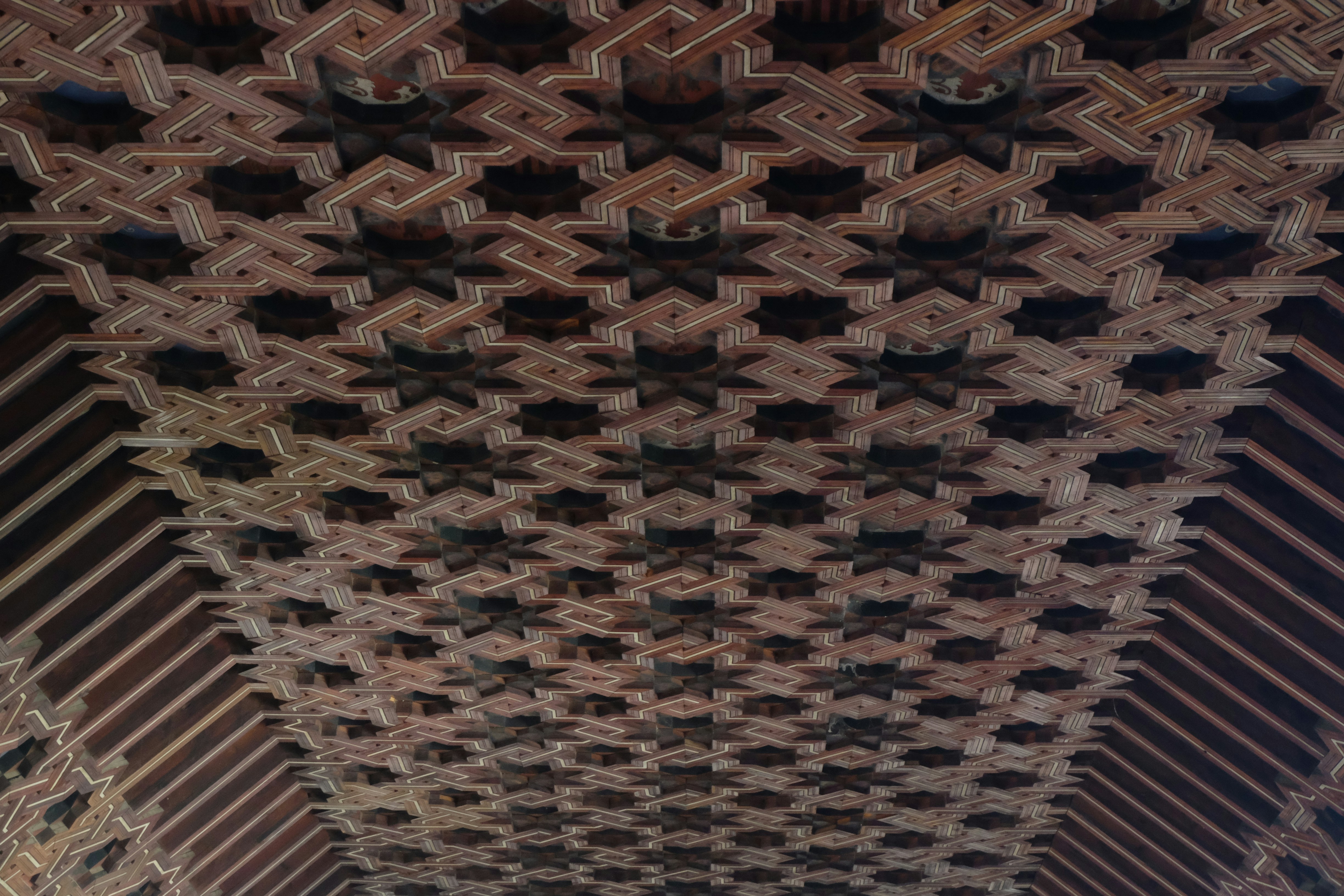 Elaborate wooden ceiling featuring intricate geometric patterns and craftsmanship. The design showcases a blend of artistry and architectural elegance.