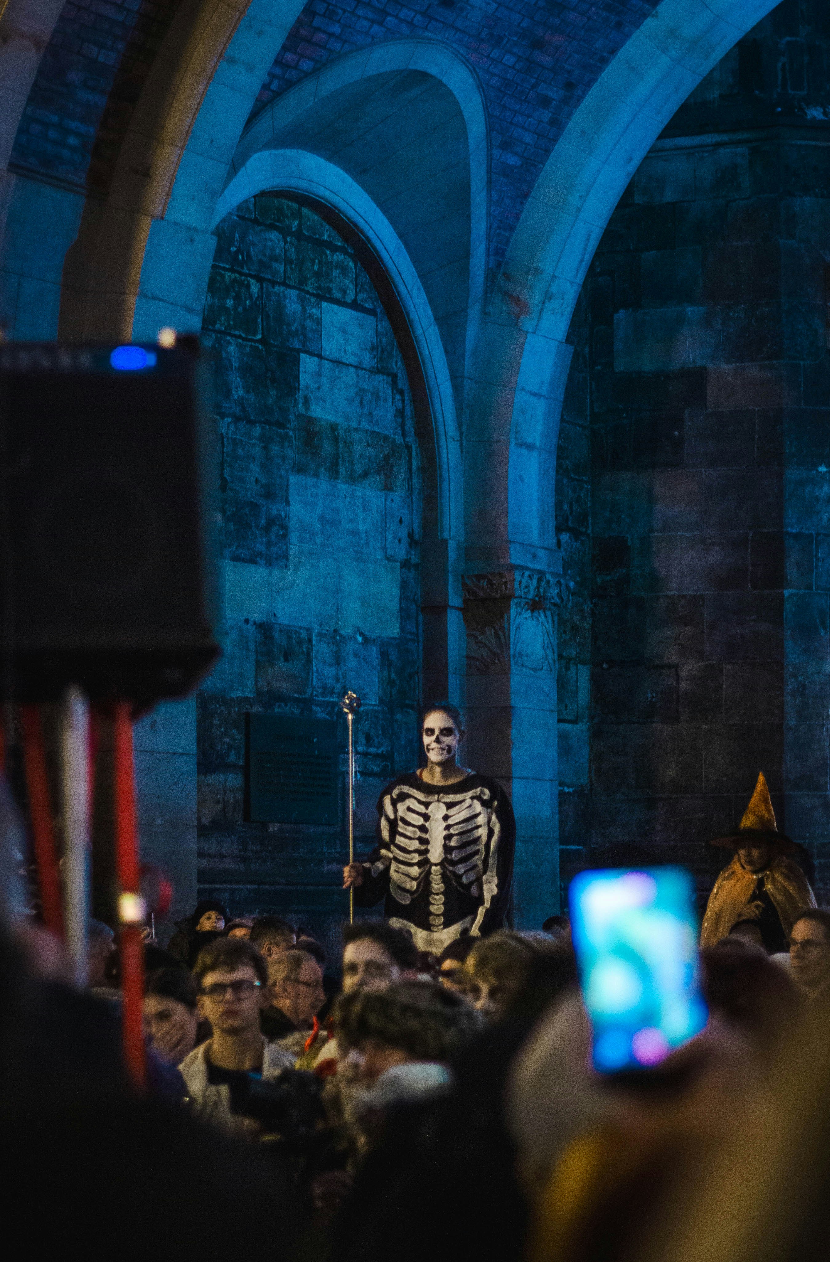 Person in skeleton costume holds staff in arched hall photo – Free ...