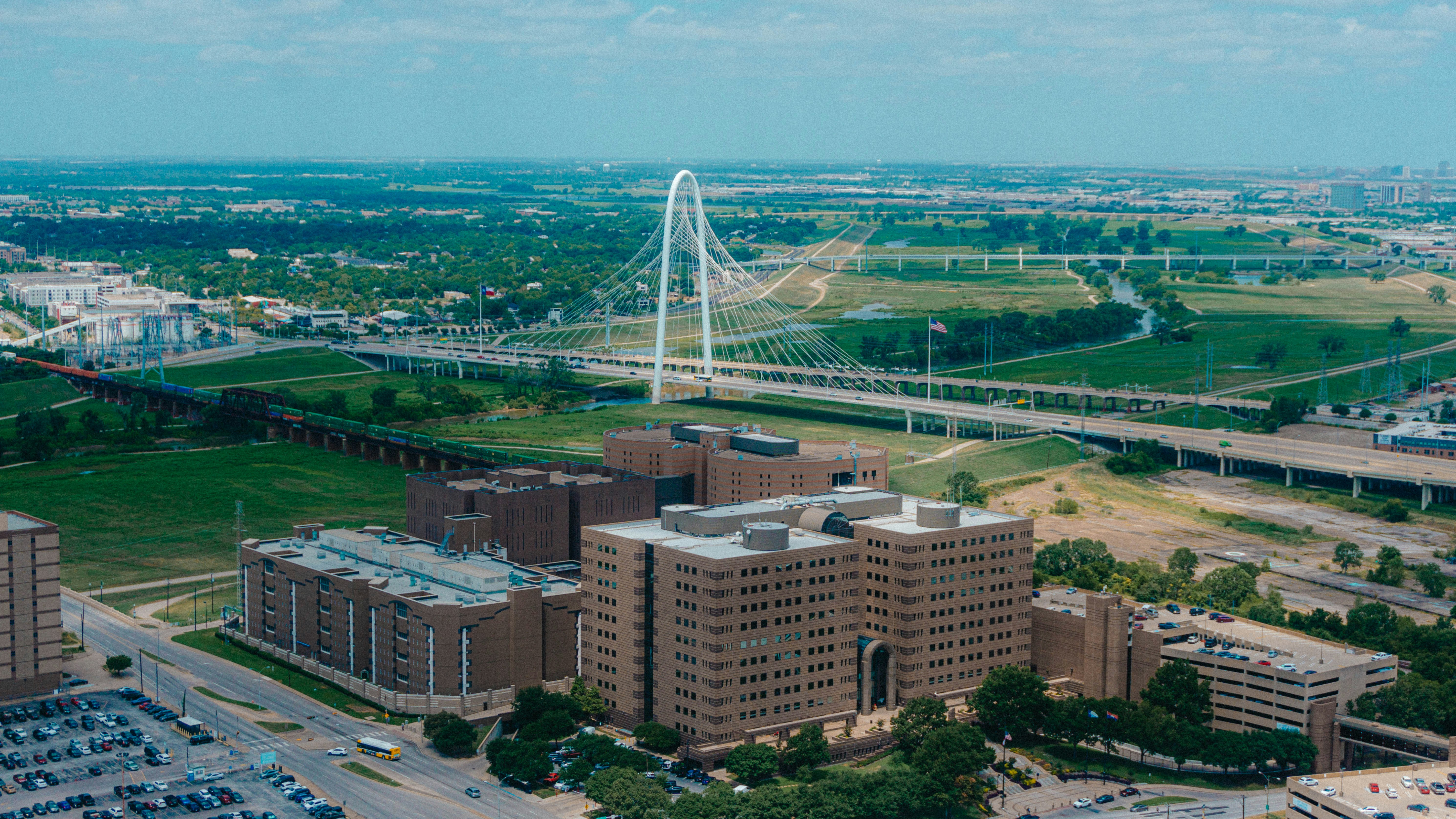 Aerial view of a sprawling cityscape featuring a modern bridge and expansive green spaces alongside urban structures.