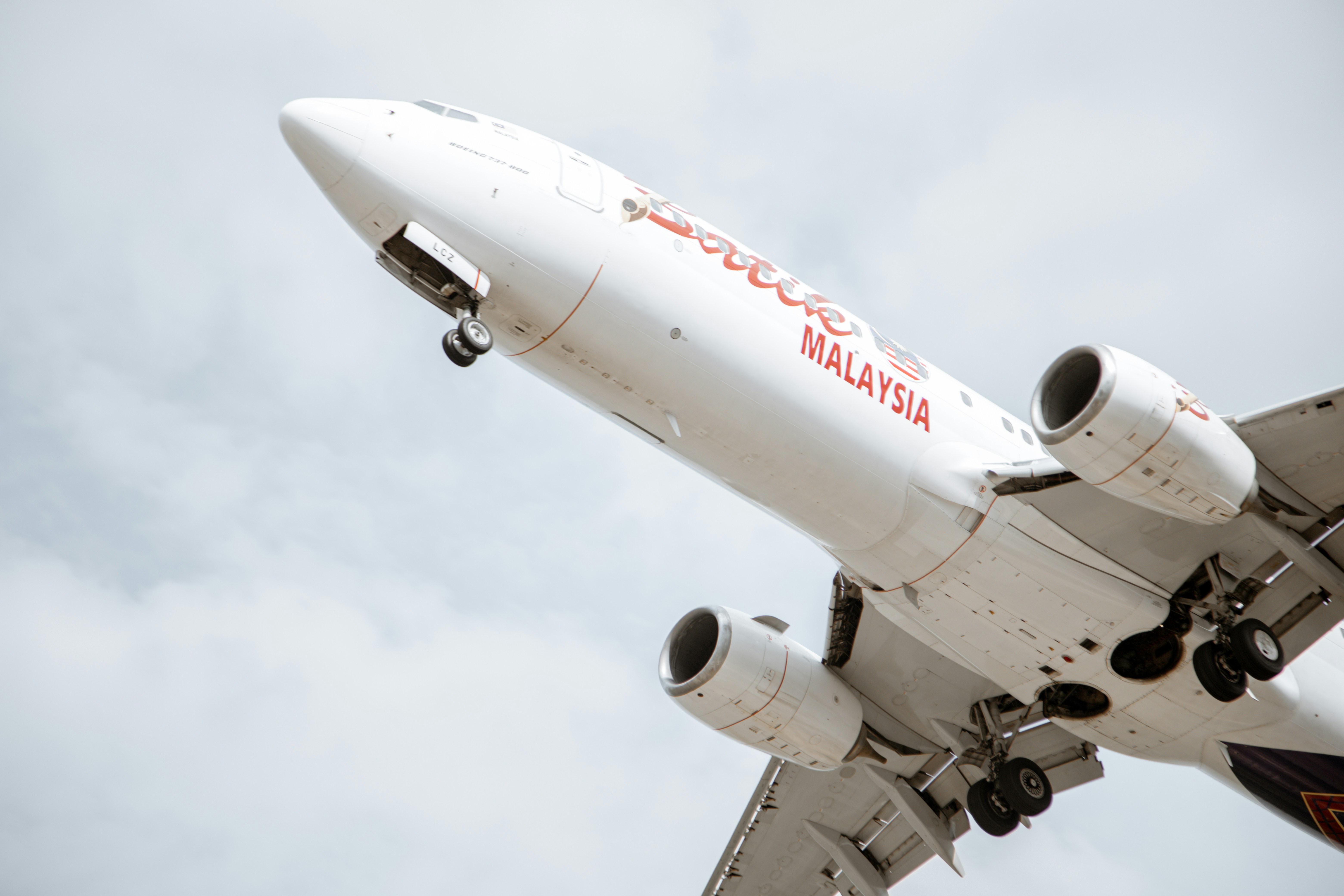A Malaysia Airlines aircraft ascends into the sky, showcasing its sleek design against a backdrop of soft, cloudy skies.
