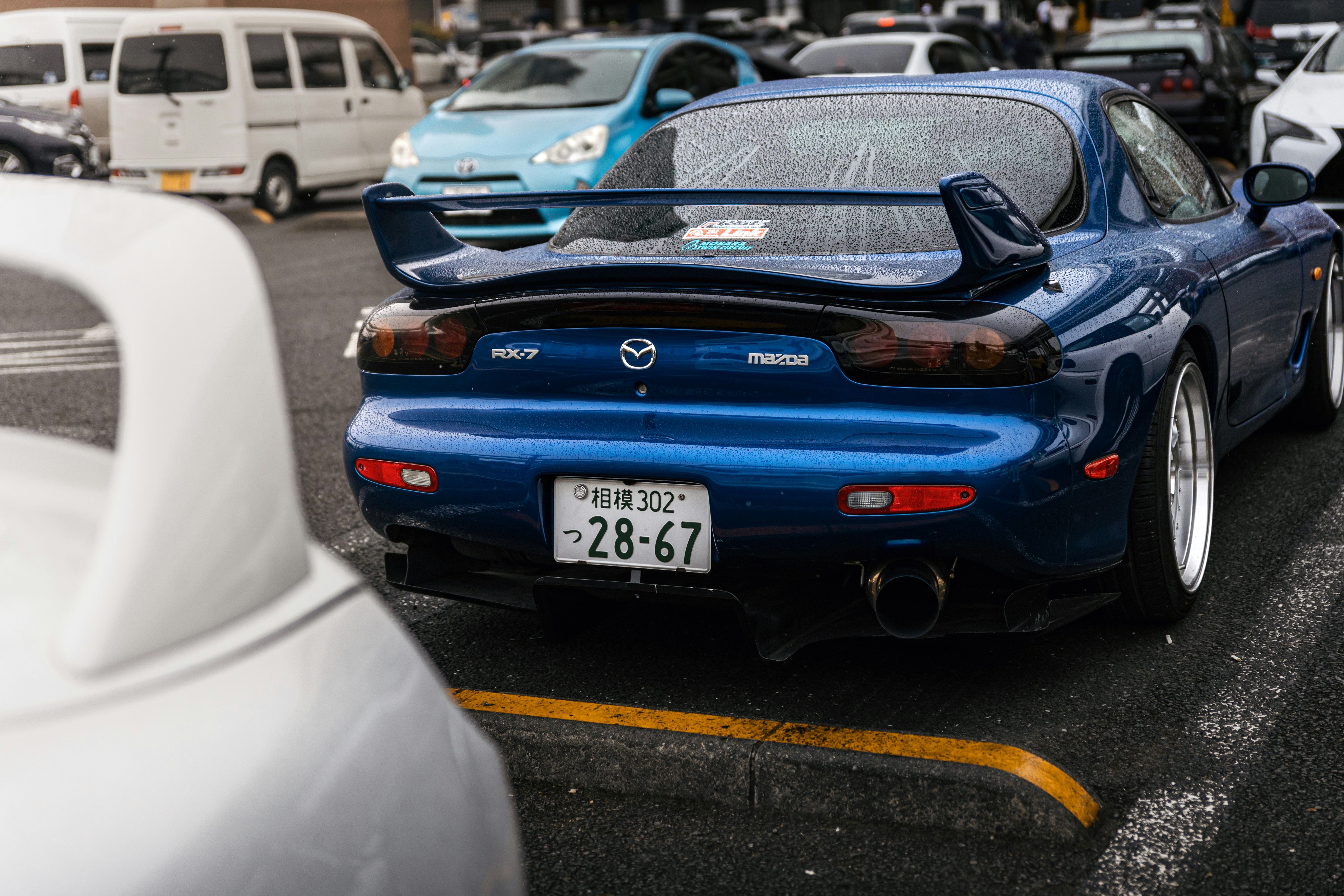 Blue Mazda RX-7 FD with a bold wing in a rain-soaked parking lot