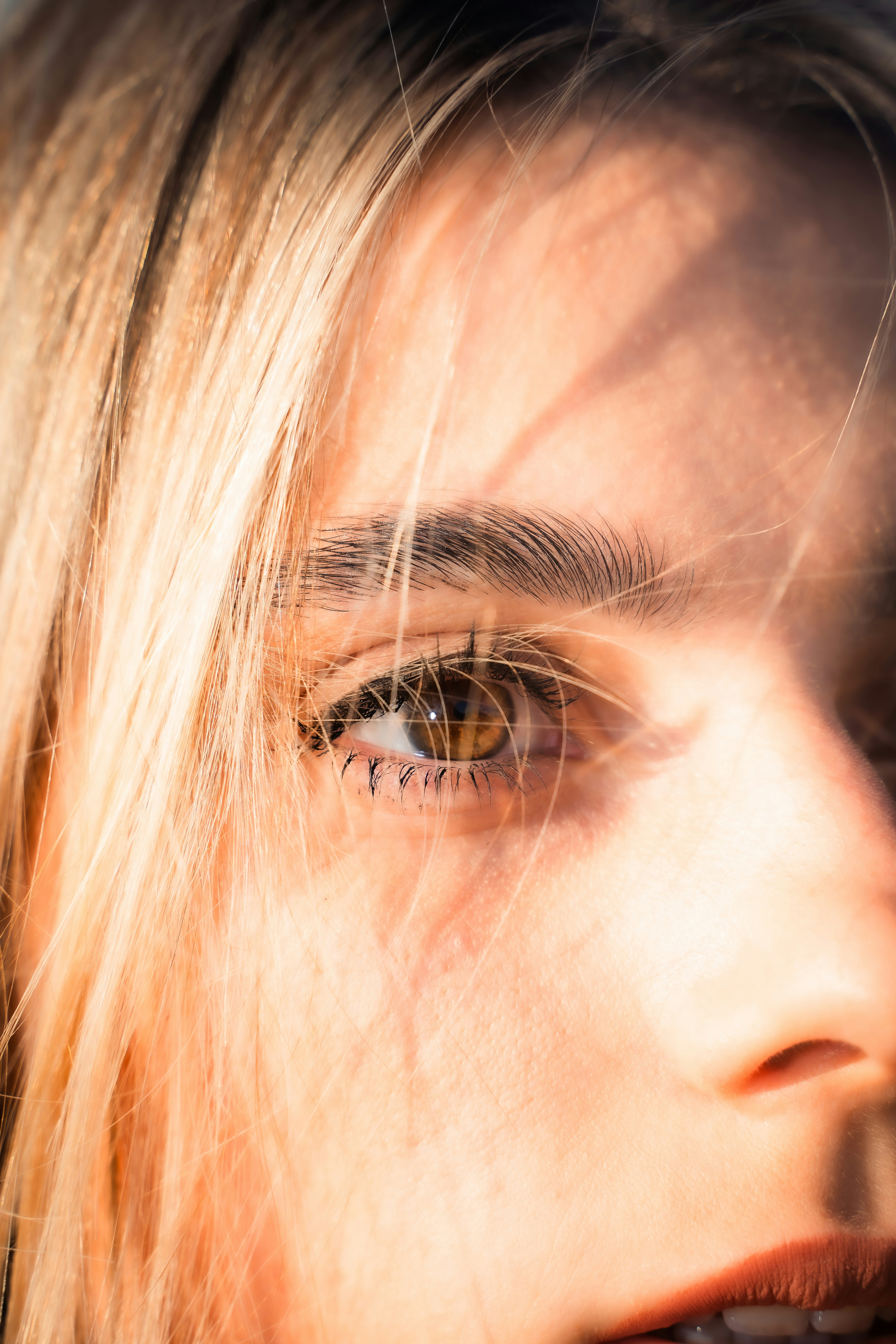 Close-up of a person's eye partially obscured by strands of hair, illuminated by soft natural light.