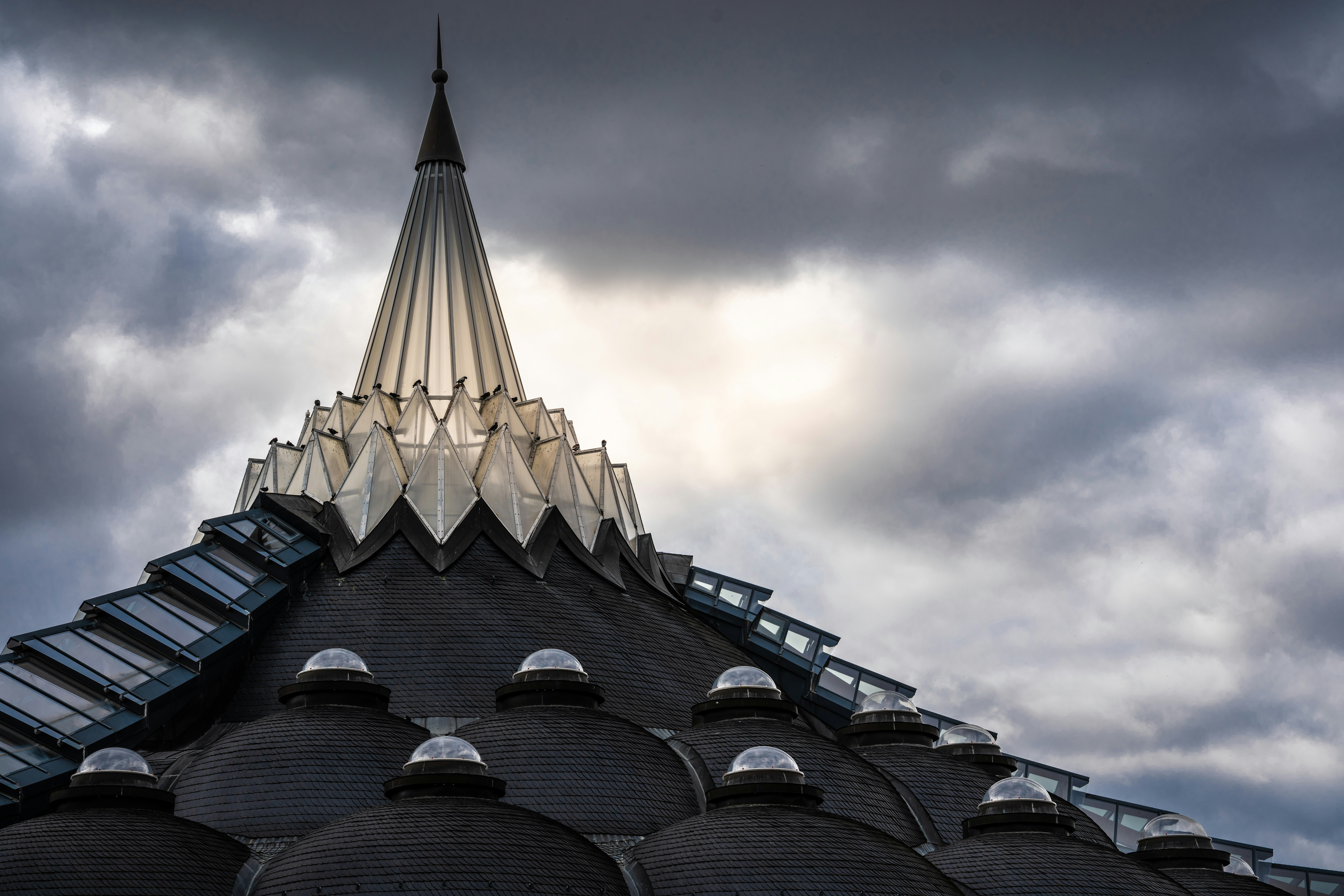 Architectural structure featuring a striking spire surrounded by a dome-shaped roof under a dramatic sky.