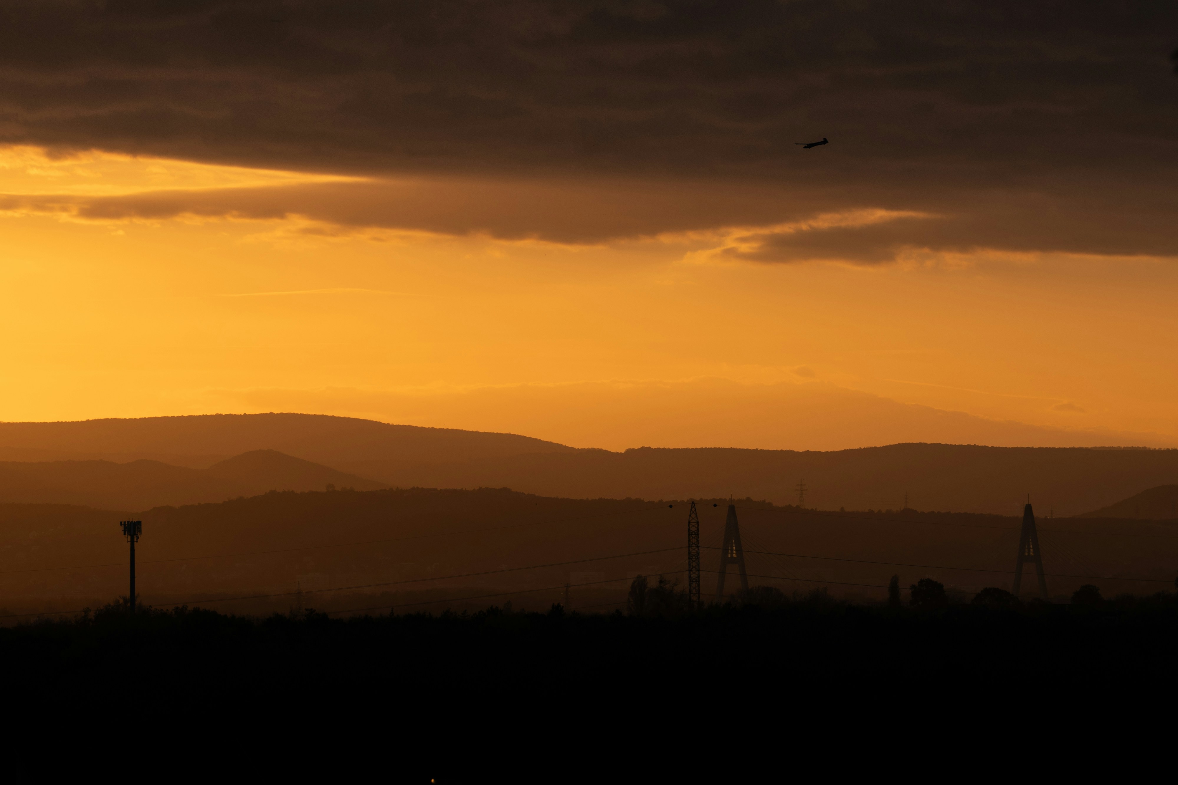 Silhouetted hills and power lines against a vibrant orange sunset, capturing the serene transition from day to night.