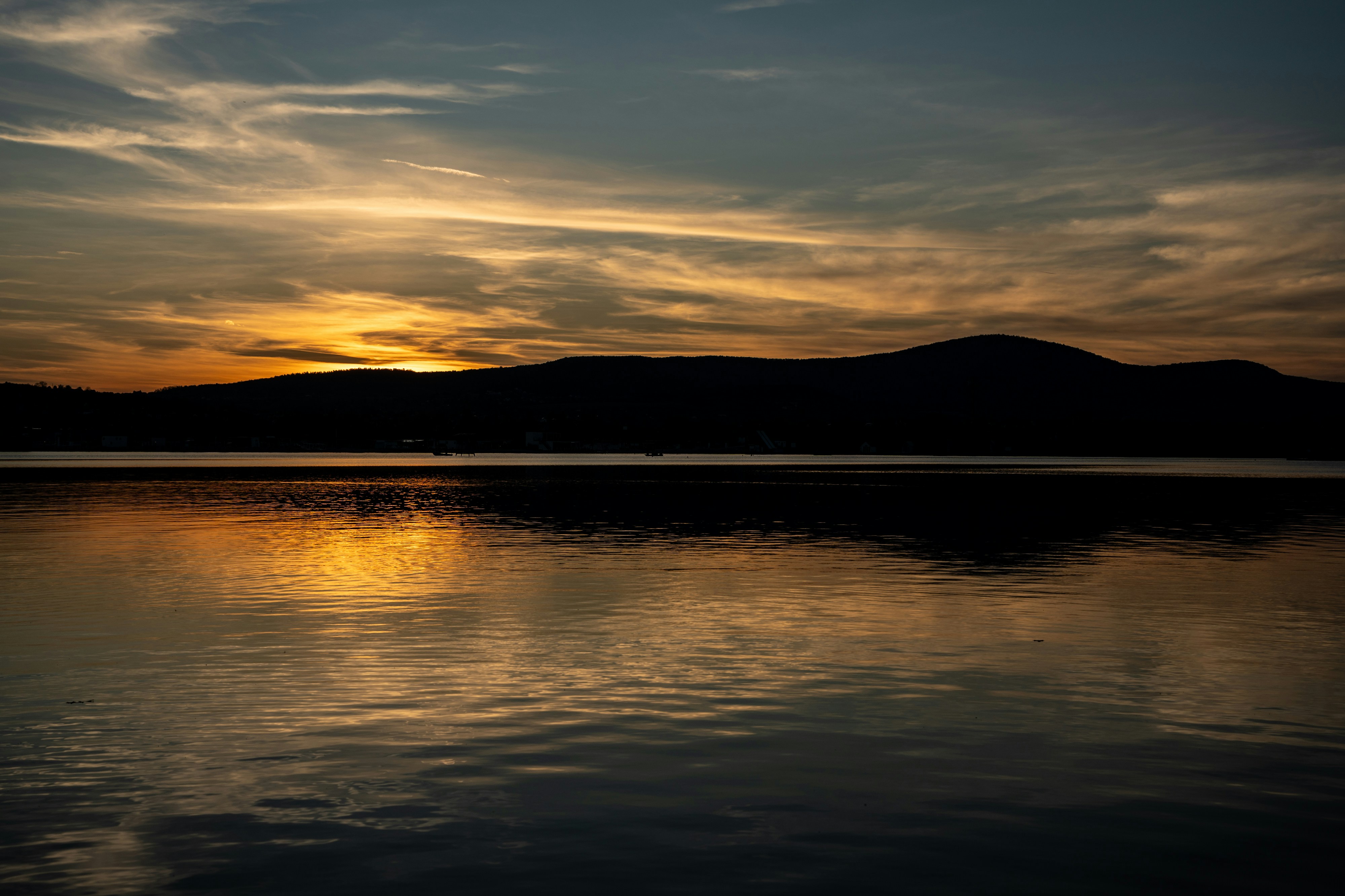 Golden hues of sunset reflecting on a tranquil lake with silhouettes of distant hills.