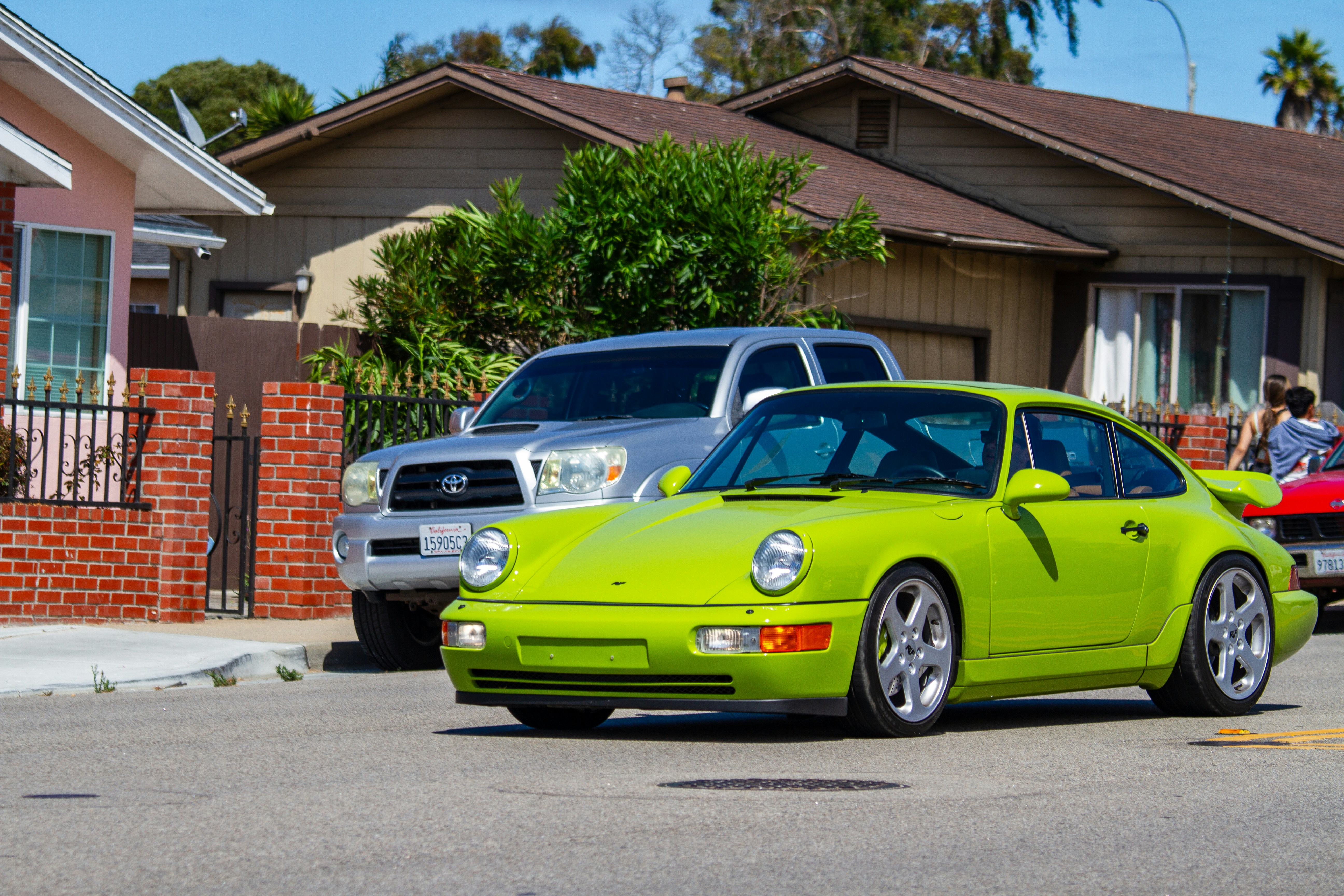 Vibrant green Porsche 911 cruising past suburban homes under clear blue skies.