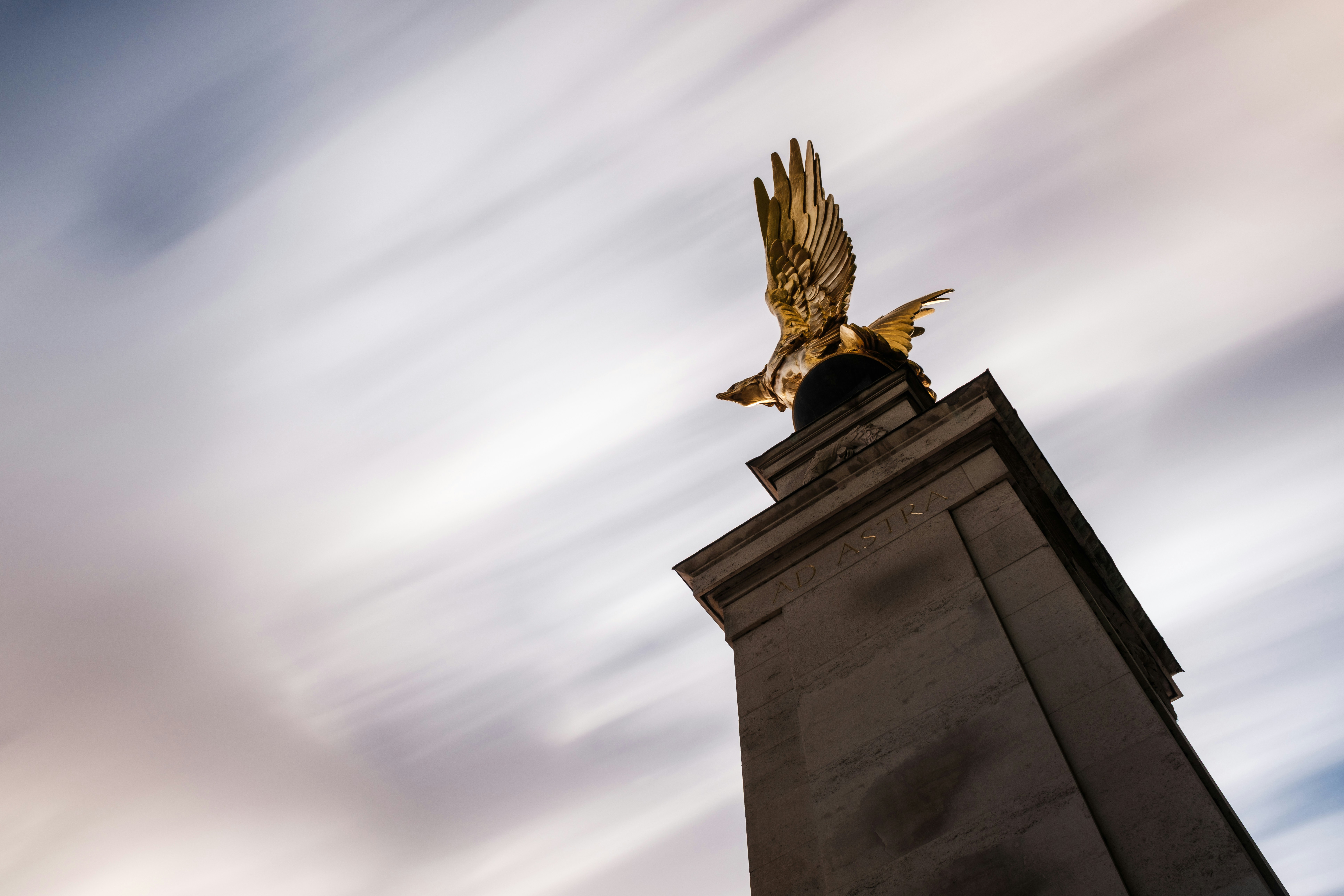 Golden eagle statue atop a stone monument against clouds.