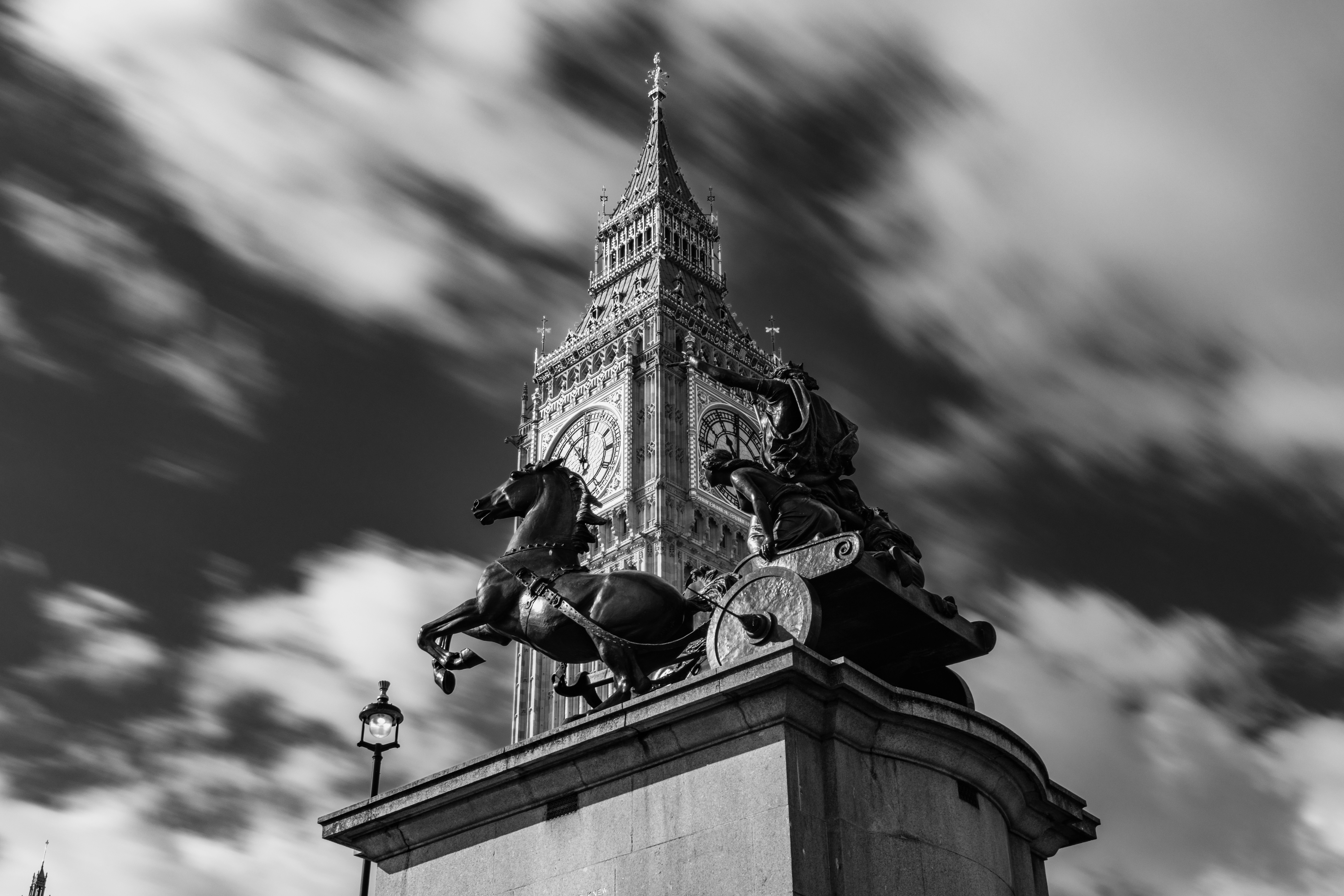 Monumental statue of a chariot and horses beneath the iconic clock tower, framed by dramatic clouds.