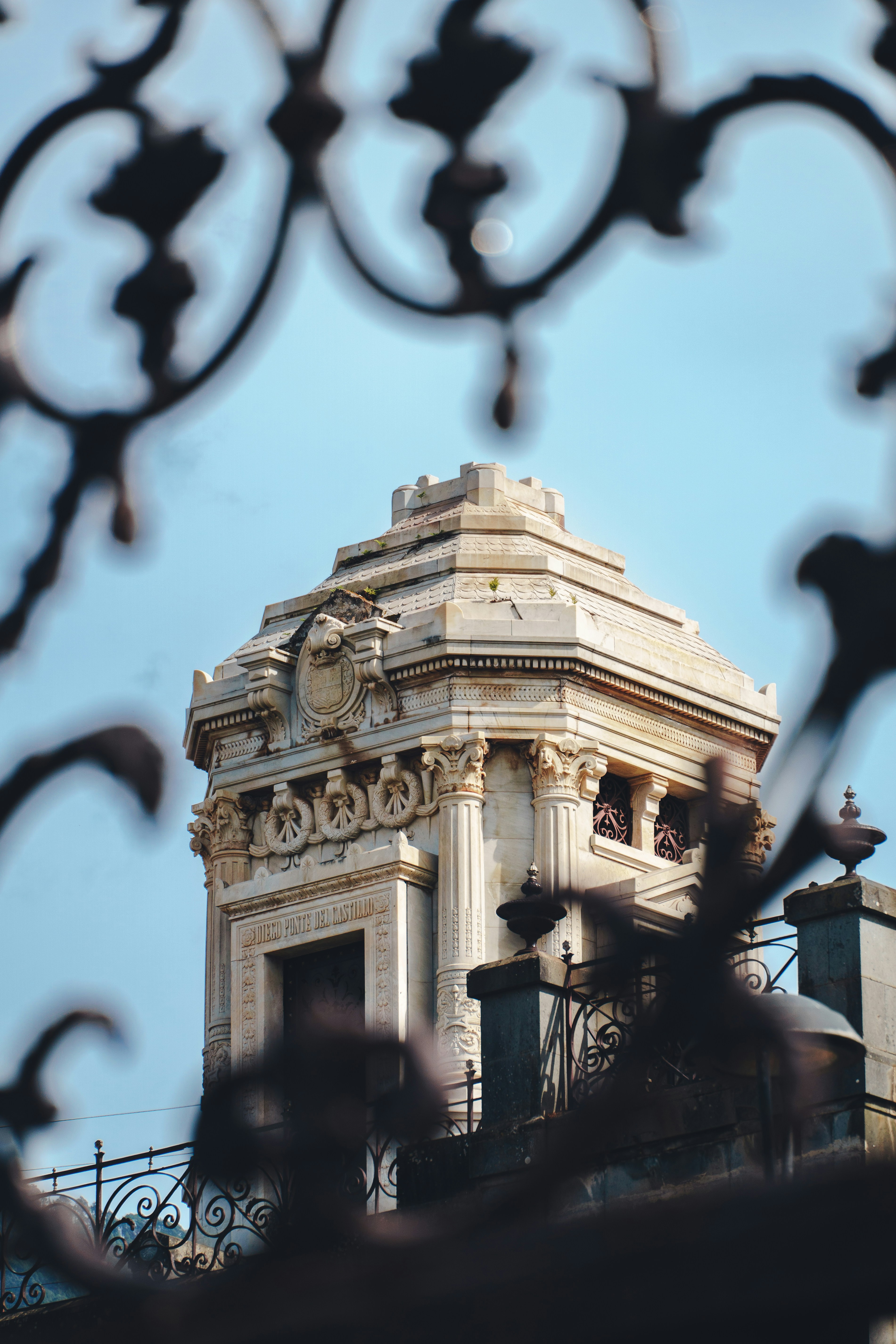 Historic building tower partially obscured by ornate ironwork, set against a clear blue sky.