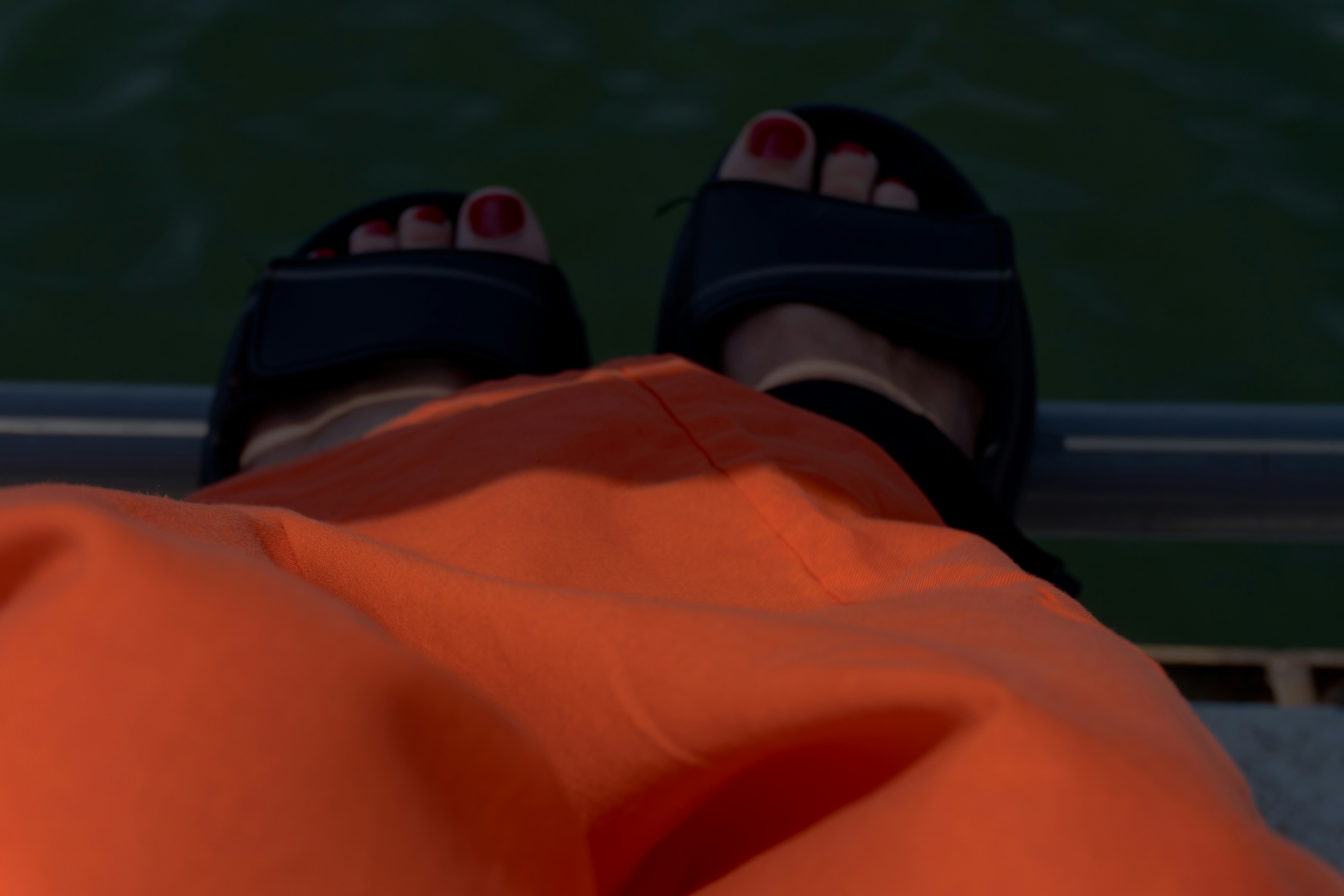 Feet in black sandals resting on a boat's edge, adorned with bright orange pants, creating a relaxed summer atmosphere.