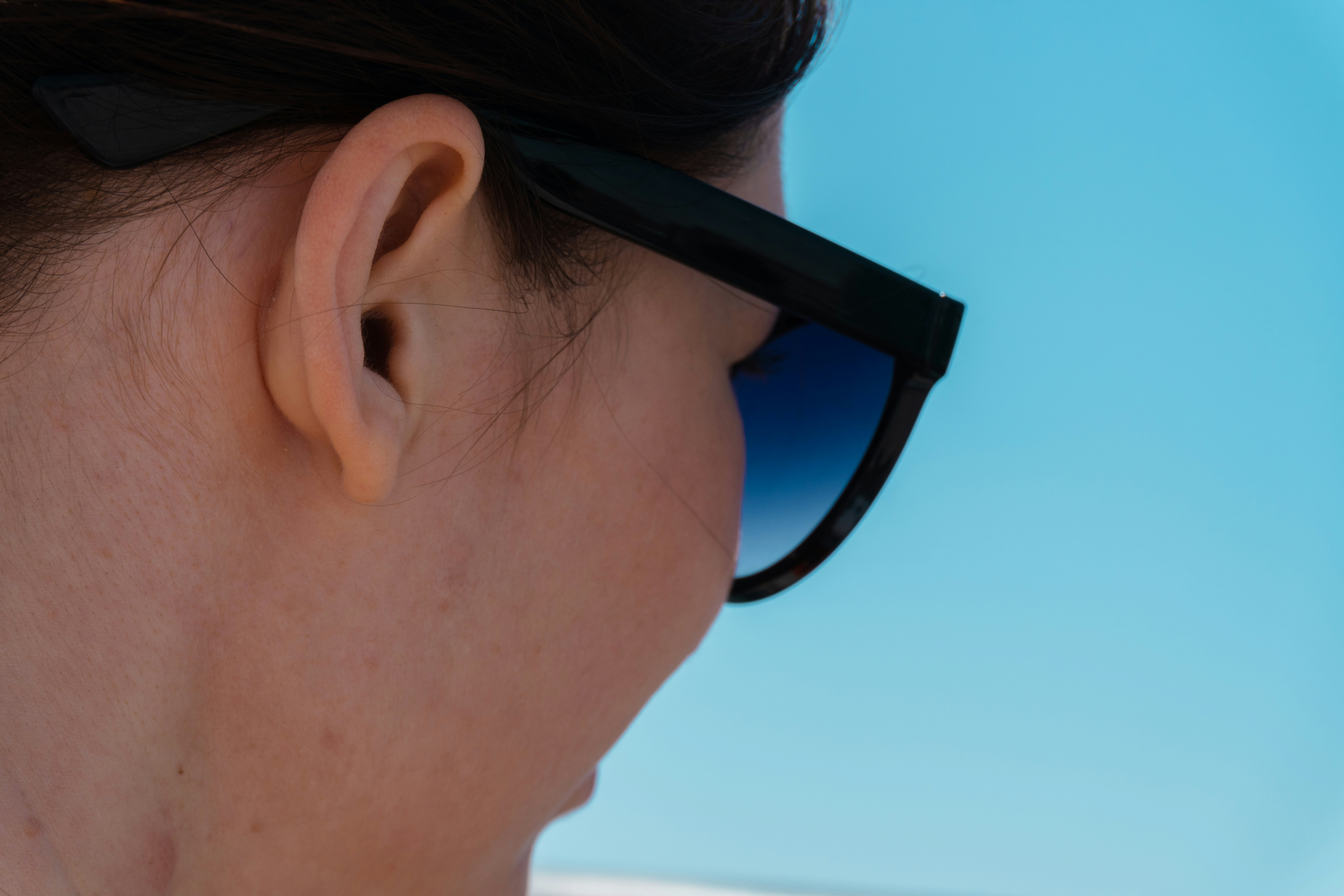 Close-up of a person wearing stylish sunglasses, with a clear blue sky in the background. The focus highlights the interplay of light and shadow on the glasses.