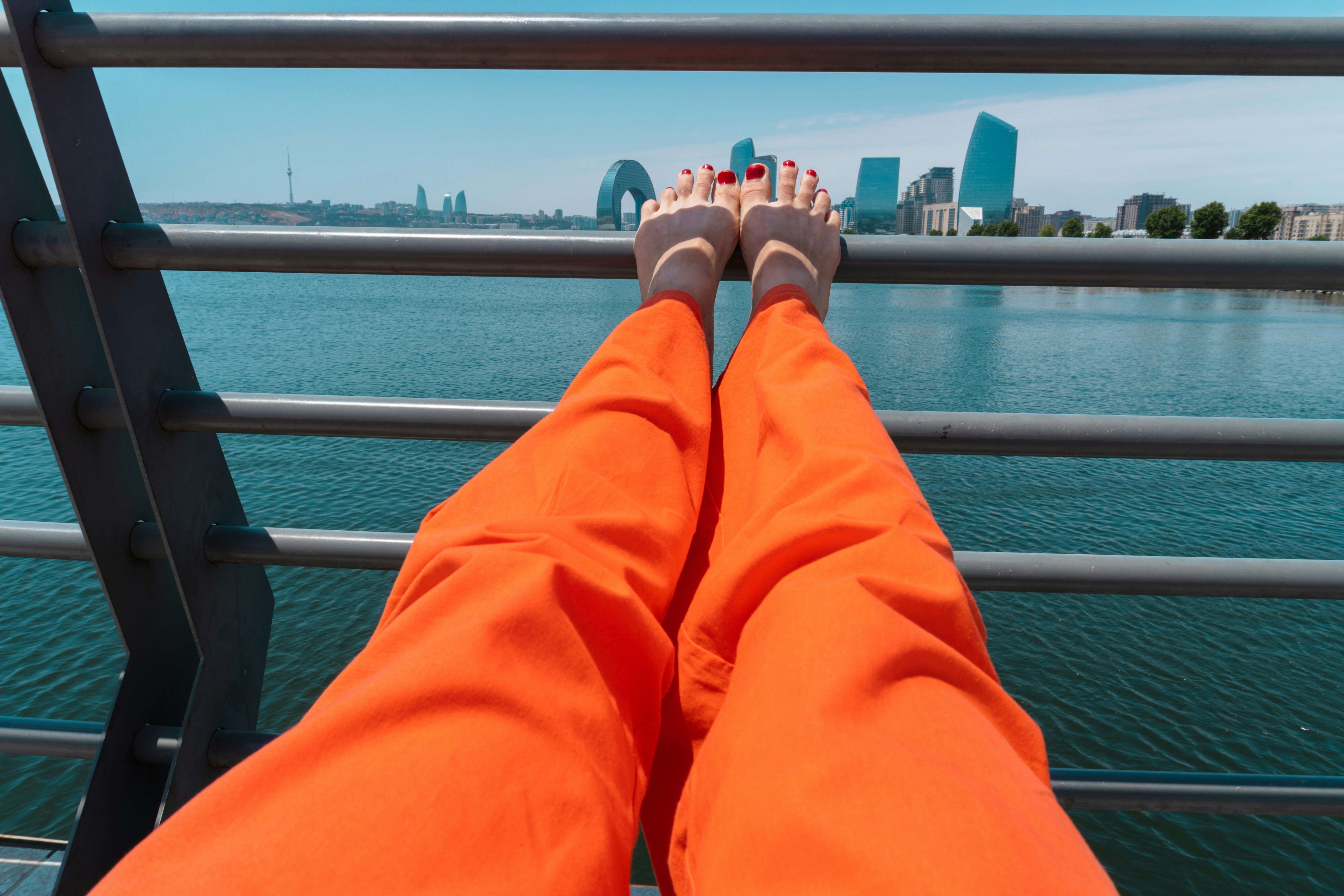 Orange-clad feet over a waterfront railing with distant city skyline