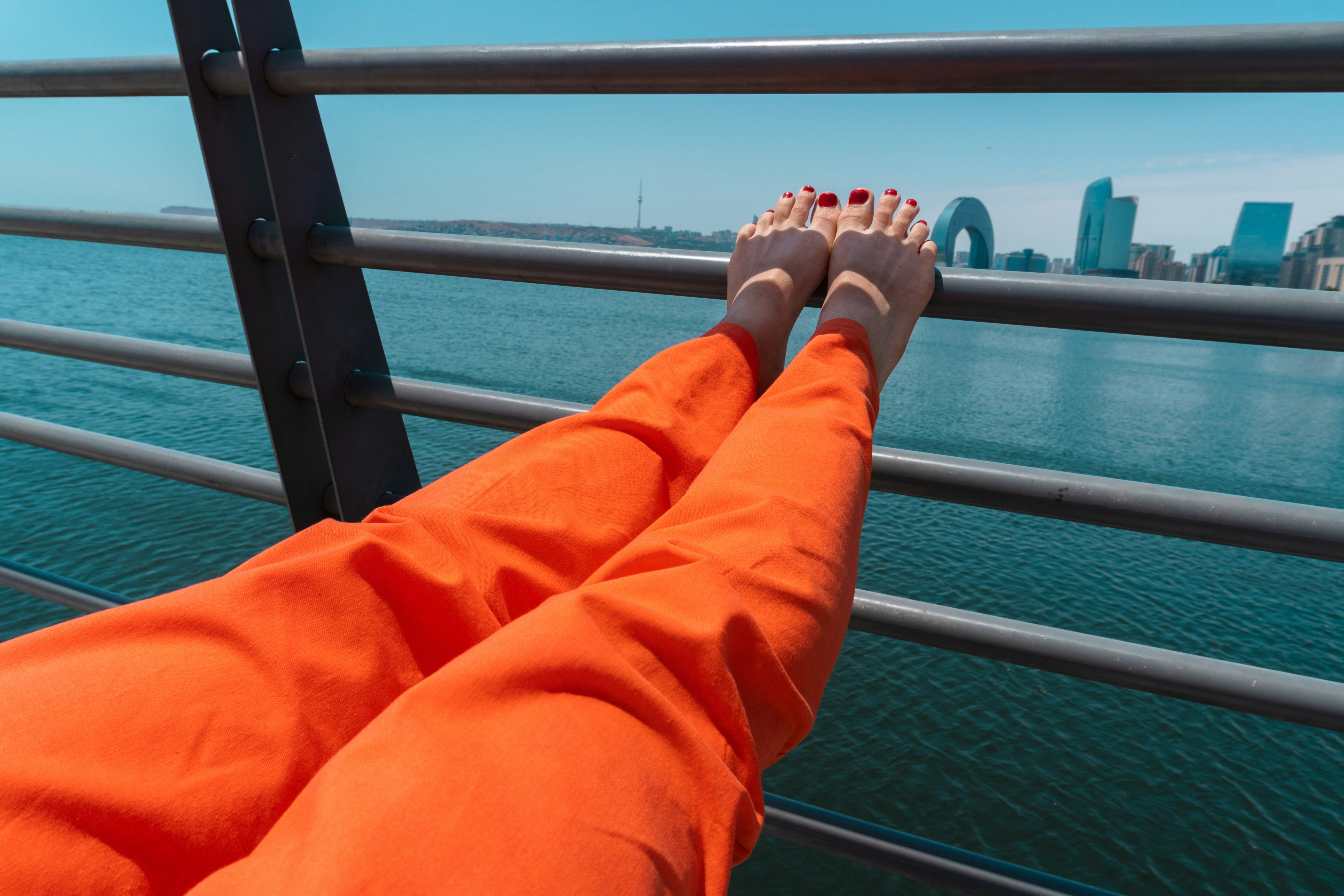 Harbor Repose: Orange-Clad Feet Drape Over a Railing as the City Drift Passes