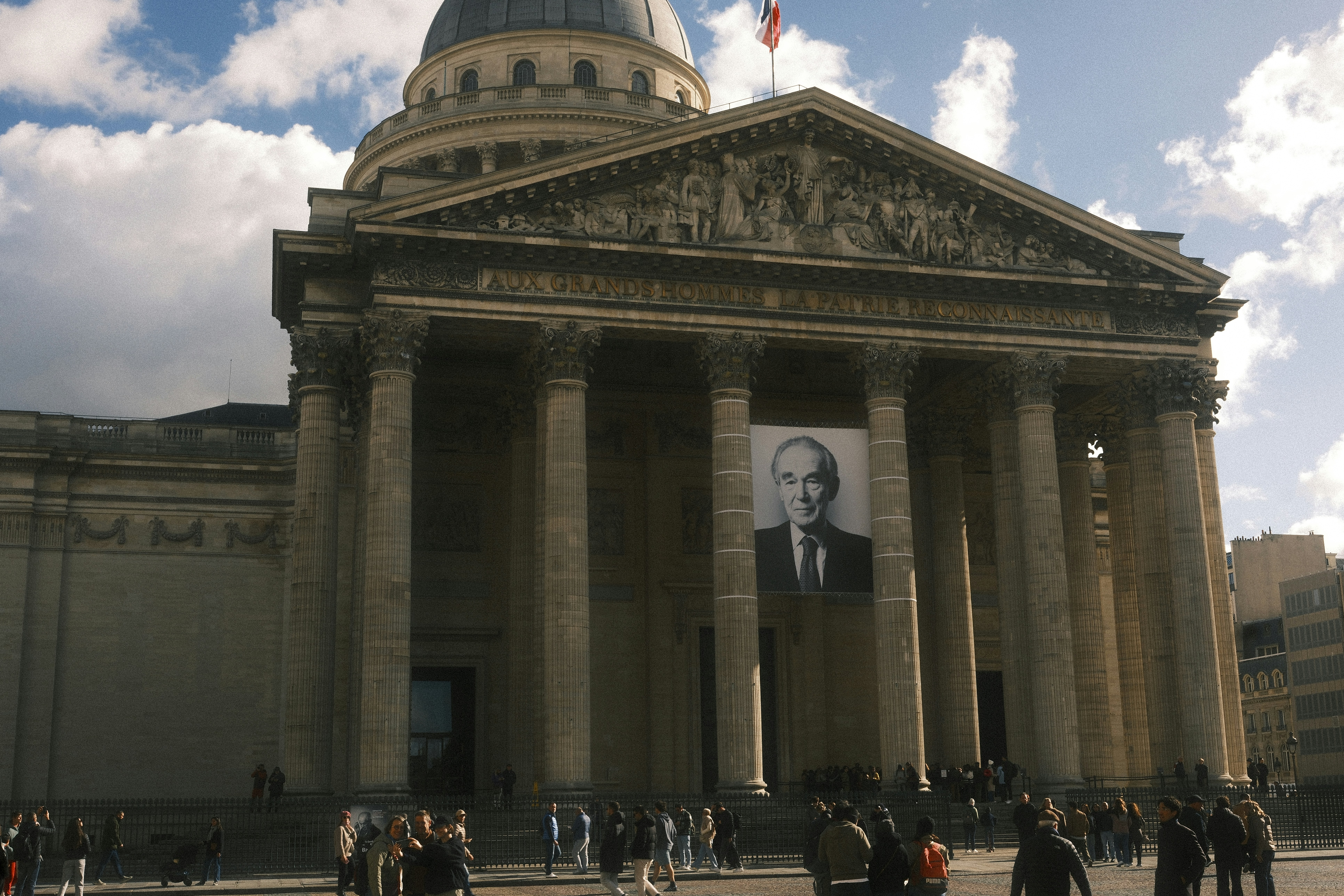 Historic building adorned with a large portrait, capturing a moment of homage amidst bustling crowds.