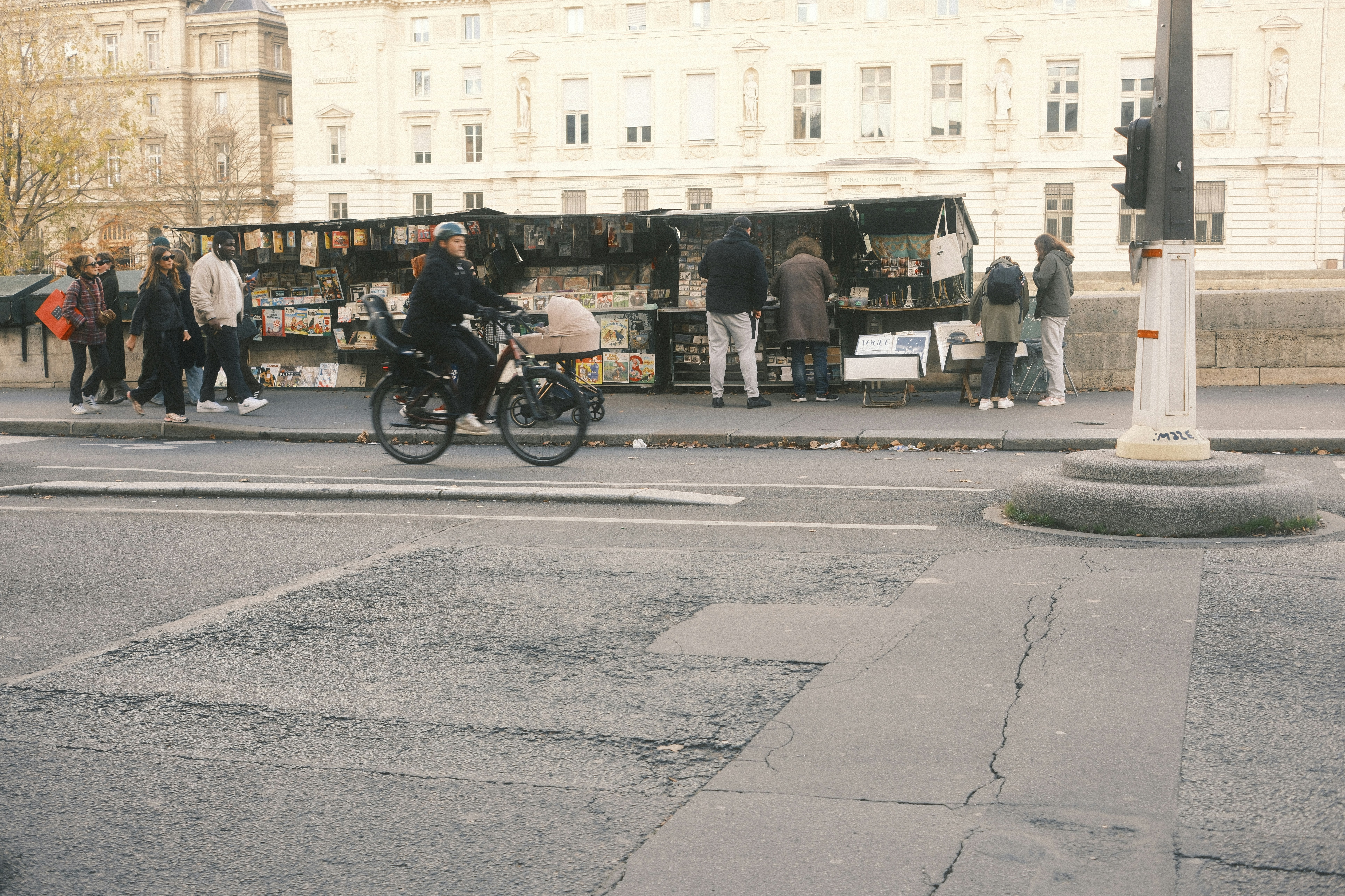A bustling street market scene with vendors displaying various items while a cyclist passes by, capturing the vibrant energy of urban life.