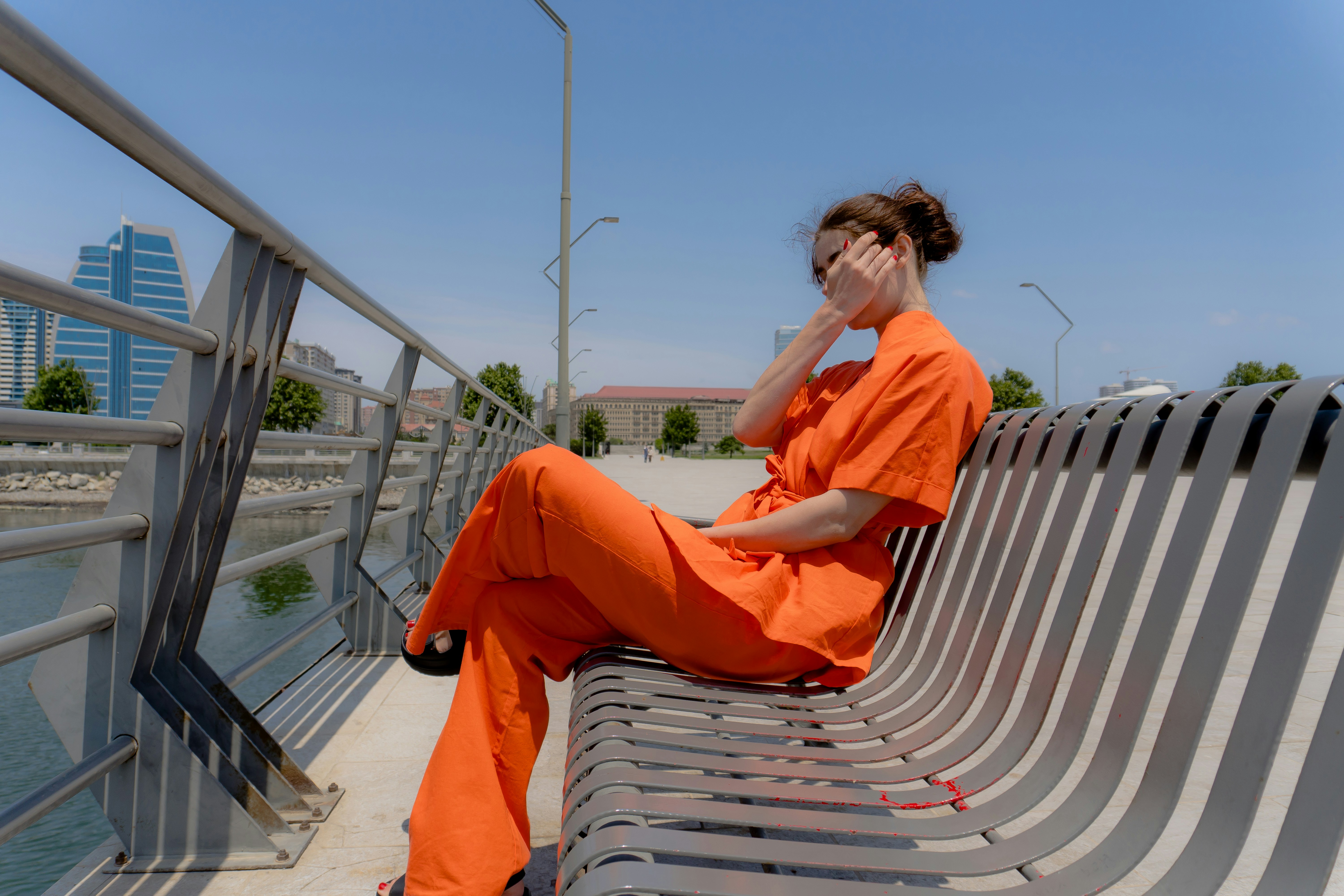 Orange-clad figure on a sunlit modern pedestrian bridge, shielding eyes from the glare