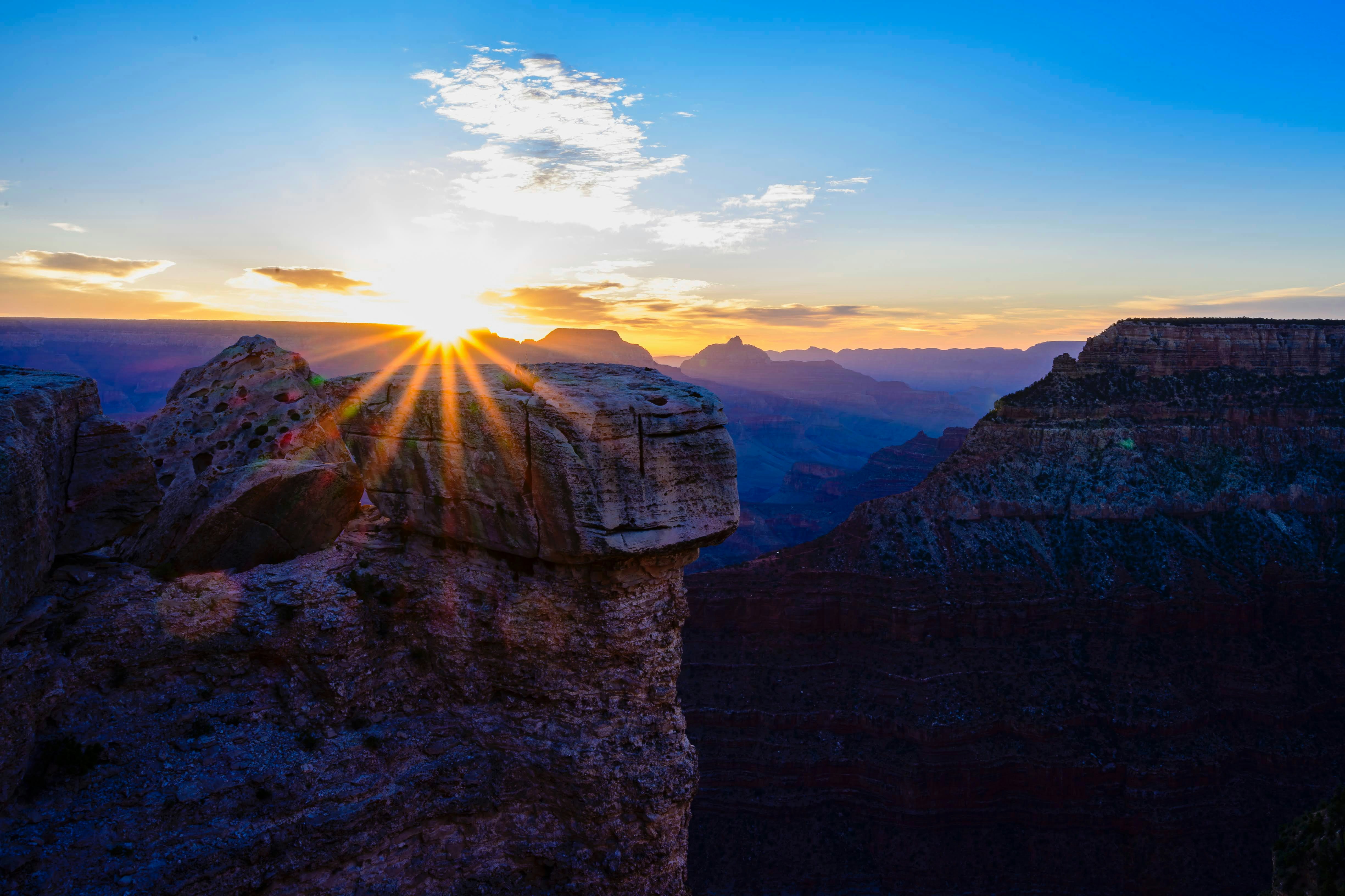 Sunrise casting rays over the Grand Canyon, highlighting the rugged rock formations and vast landscape. The scene captures the serene beauty of nature at dawn.