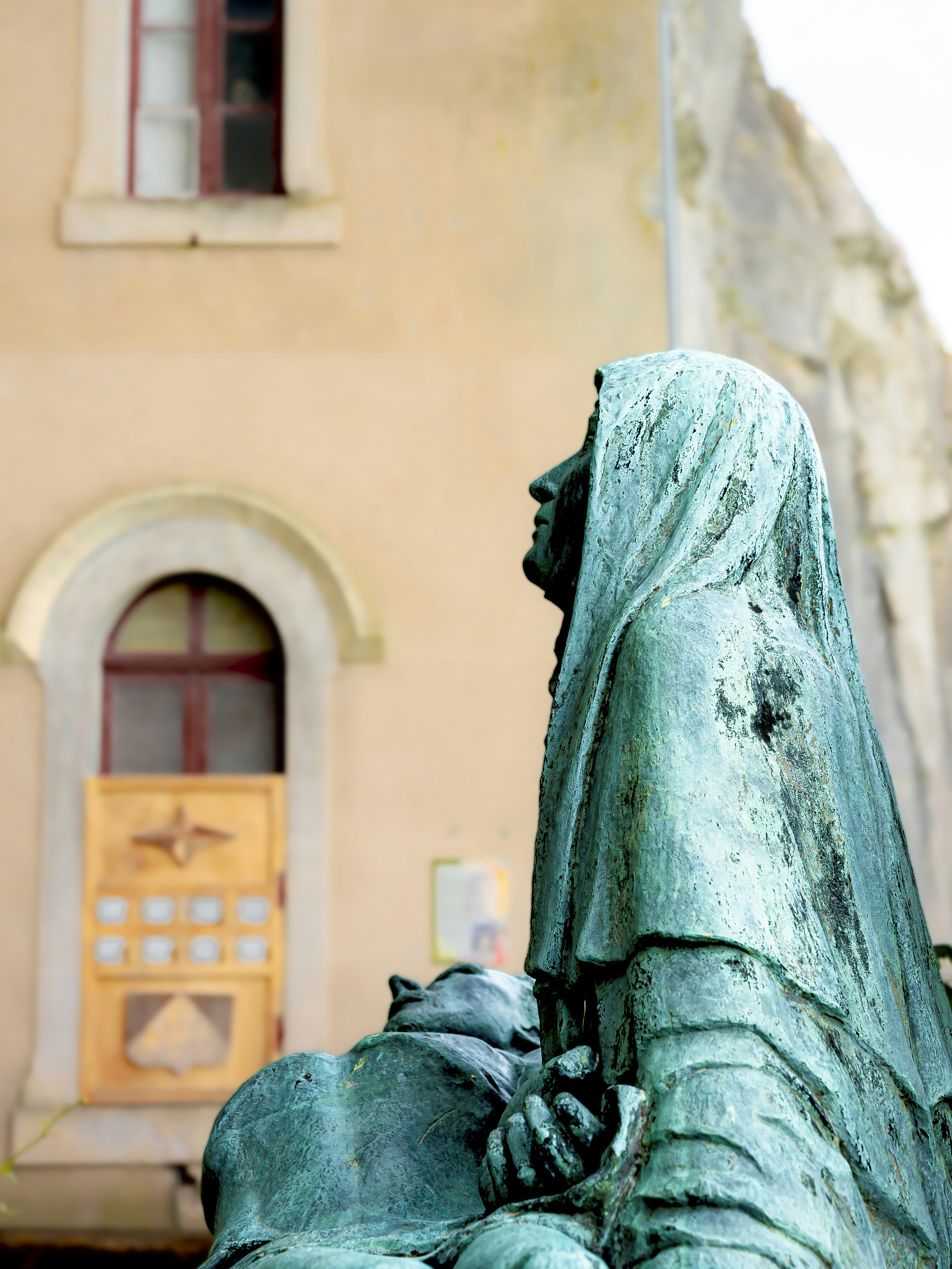 A weathered bronze statue of a robed figure looks upward.