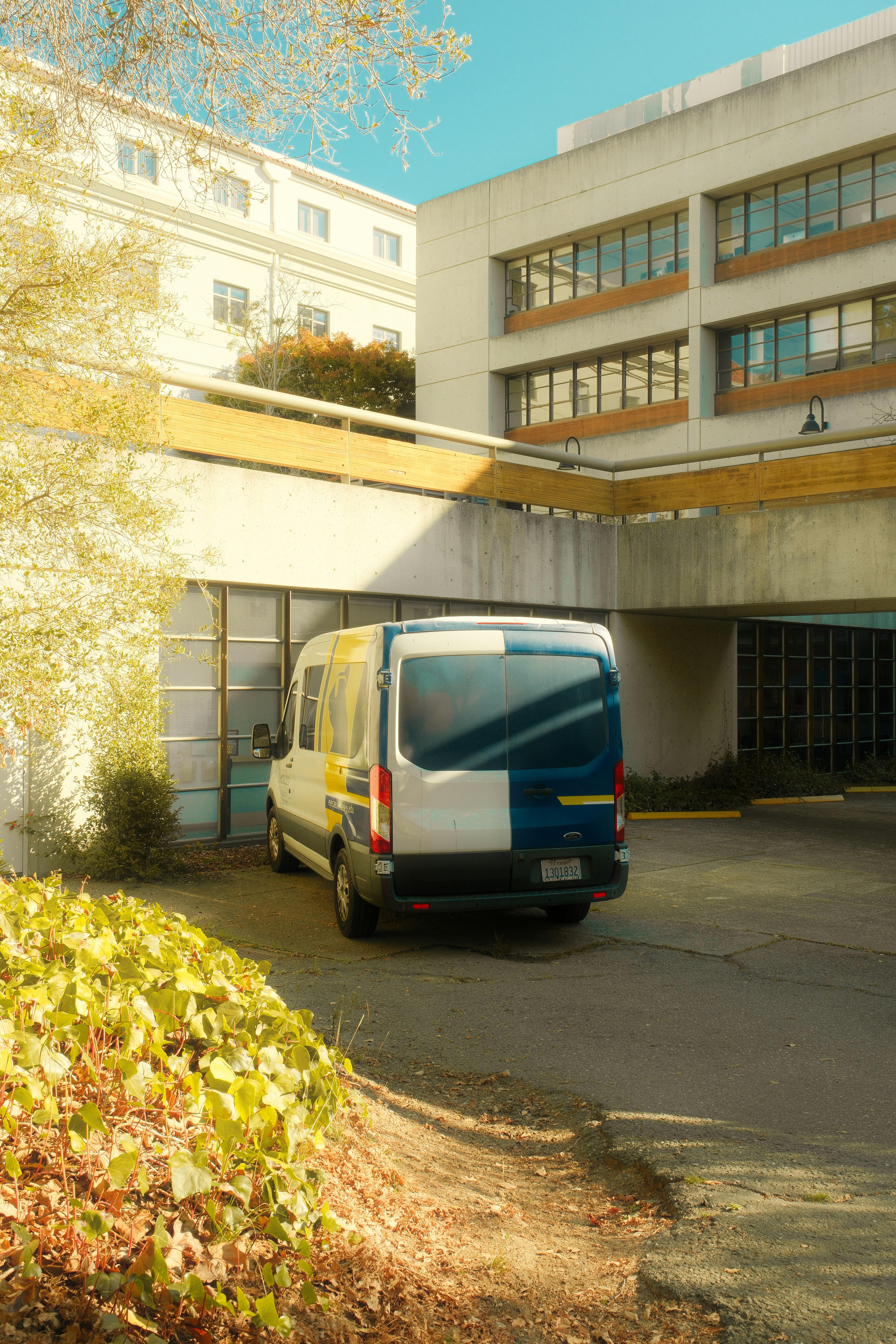 A parked delivery van nestled in a sunlit urban setting, surrounded by greenery and modern architecture.