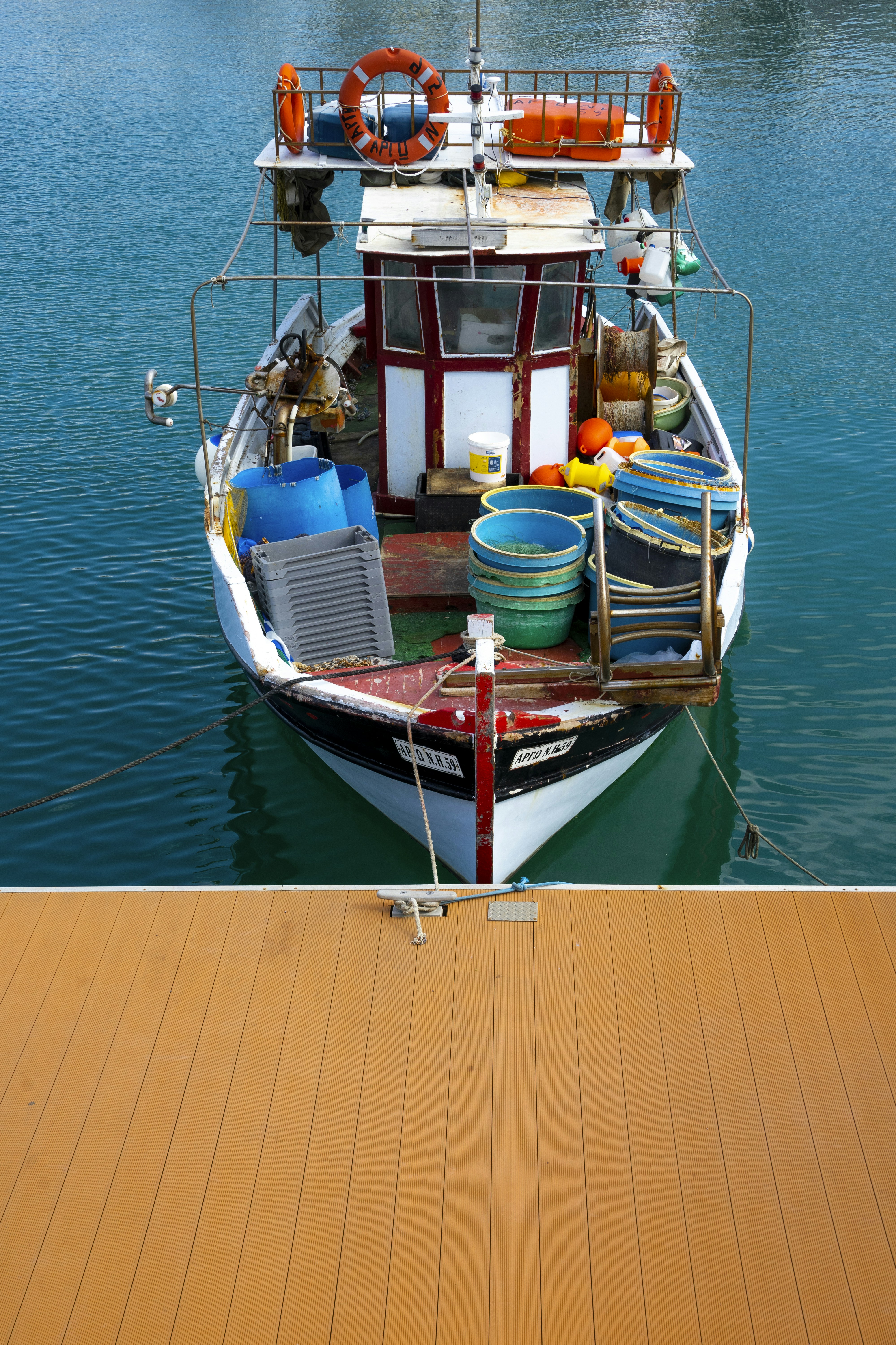 Fishing boat moored at a dock, surrounded by colorful containers and calm waters. The scene captures the essence of maritime life.