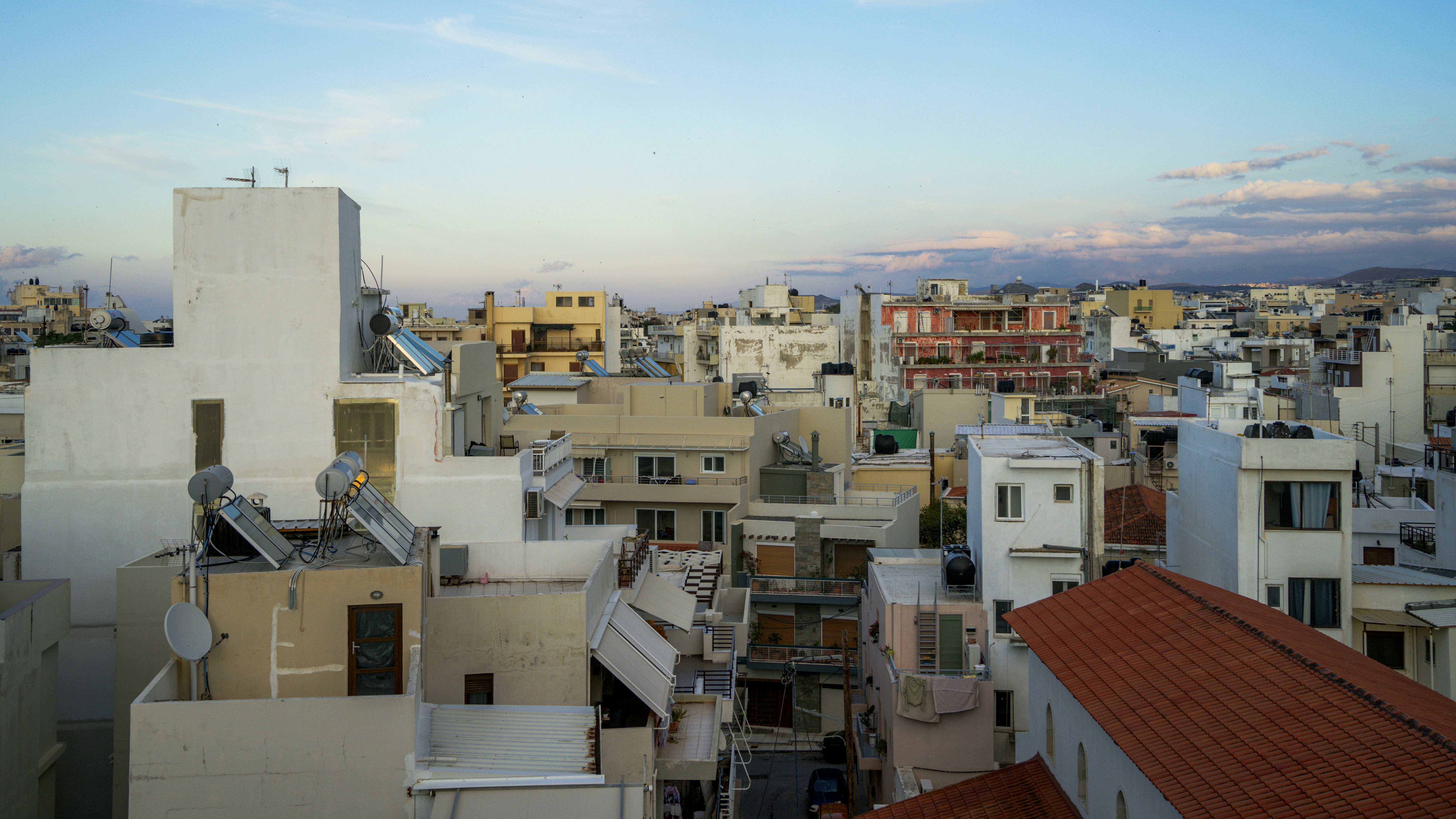 A sprawling view of urban rooftops, showcasing a mix of architectural styles and colors under a soft evening sky.