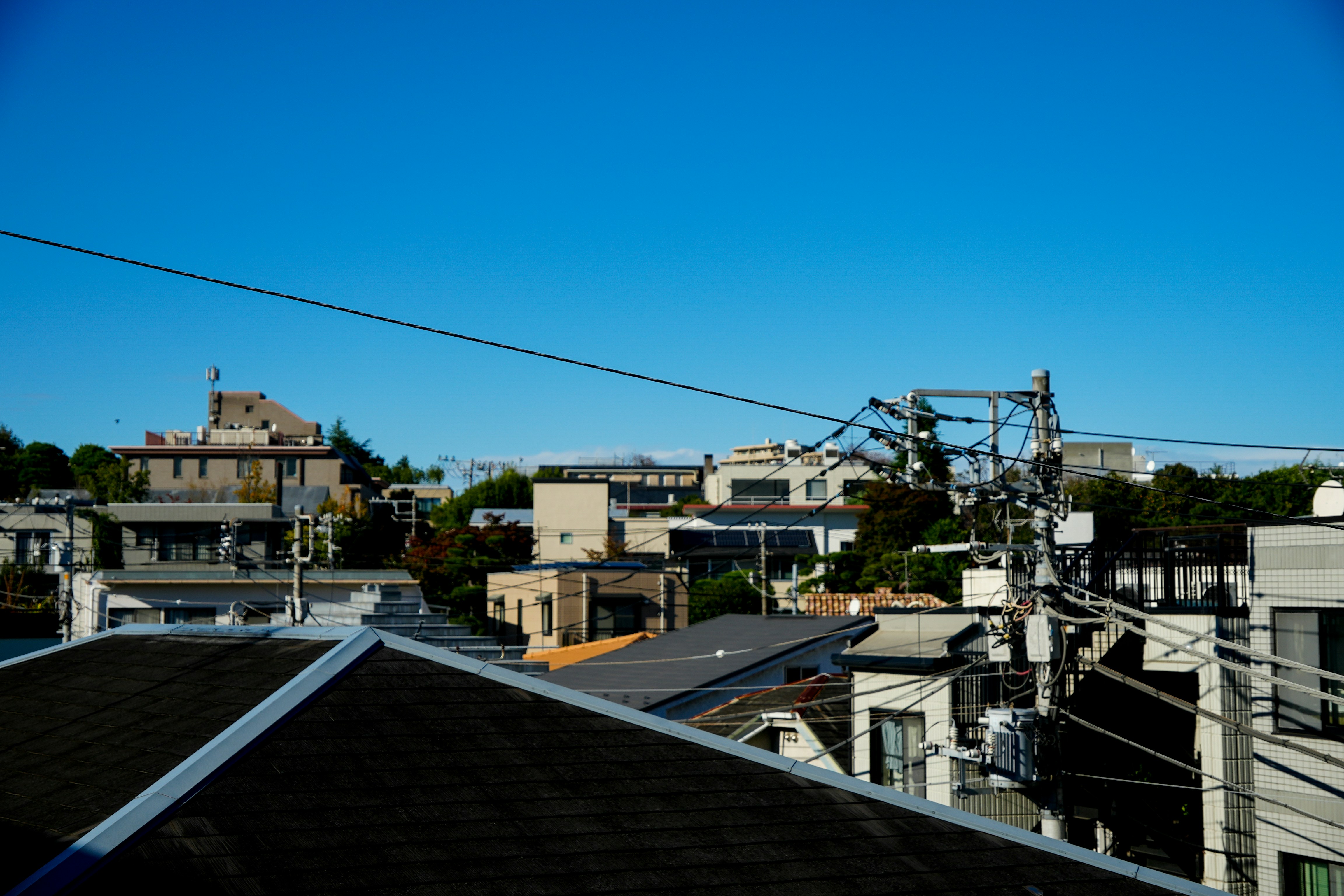A vibrant cityscape showcasing rooftops and utility lines against a clear blue sky. The scene illustrates the intricate layout of urban architecture.