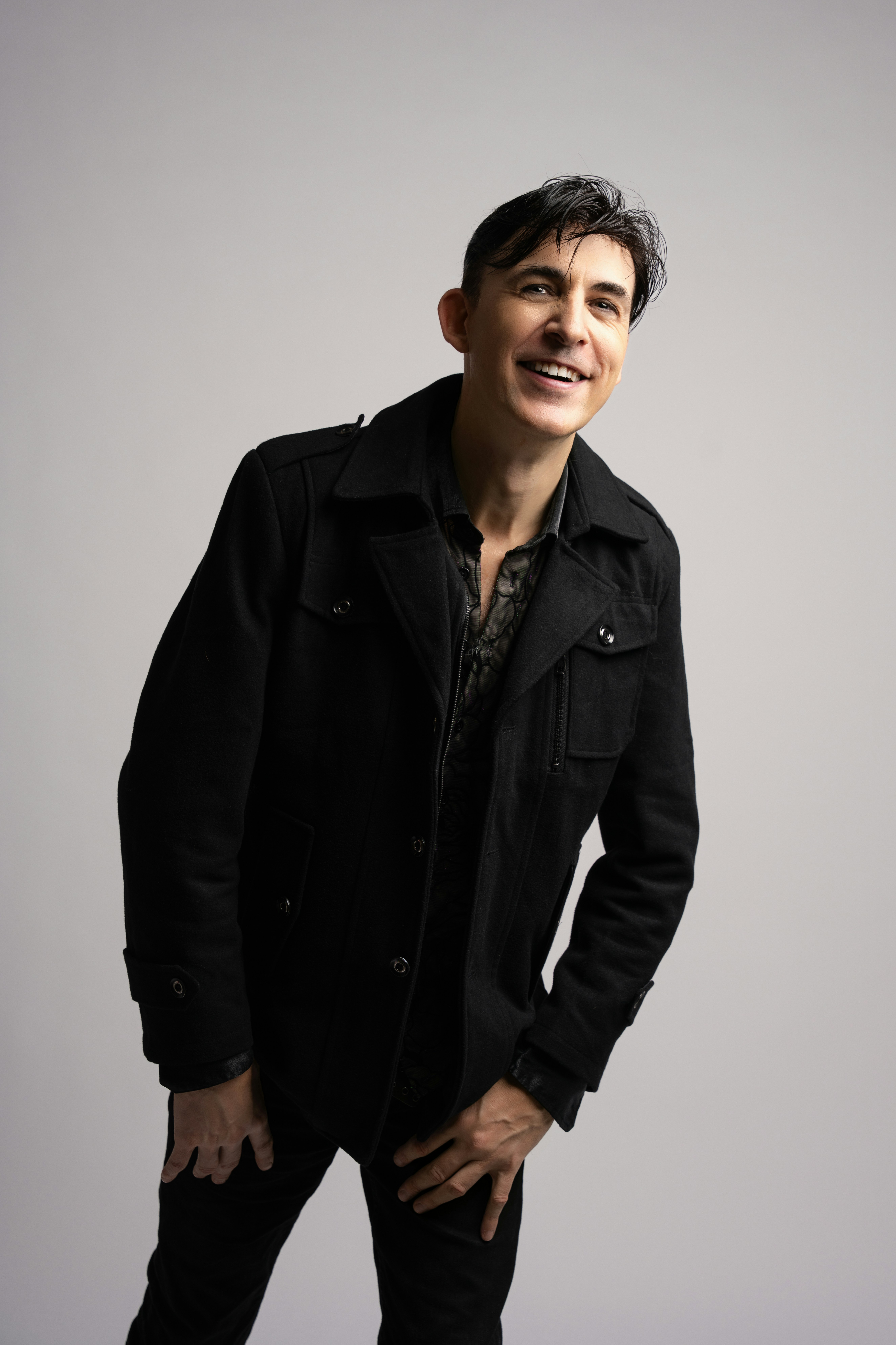 Man in black coat smiling against a gray background