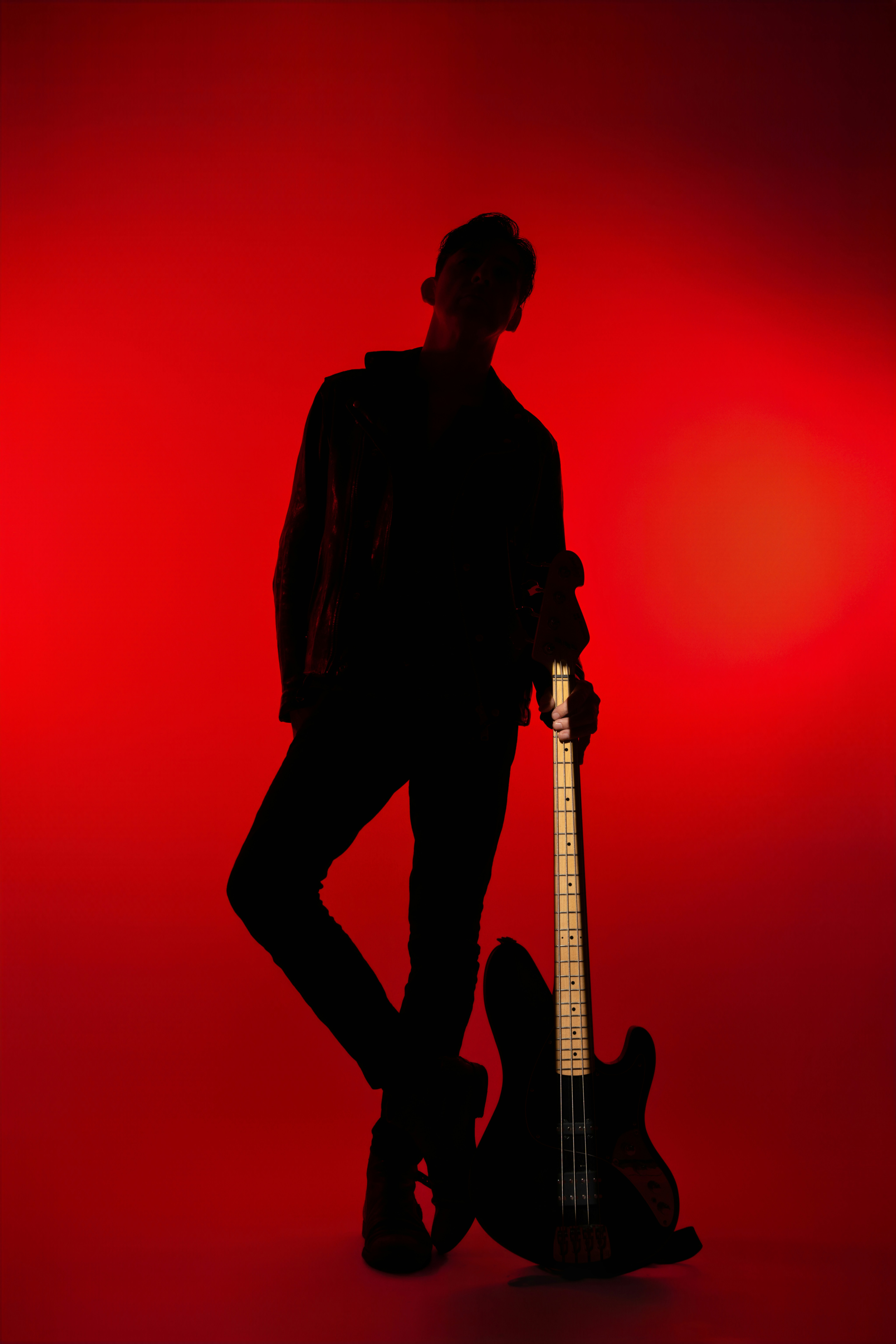 Silhouette of a bassist against a vibrant red background, exuding a sense of musical intensity and artistic expression.