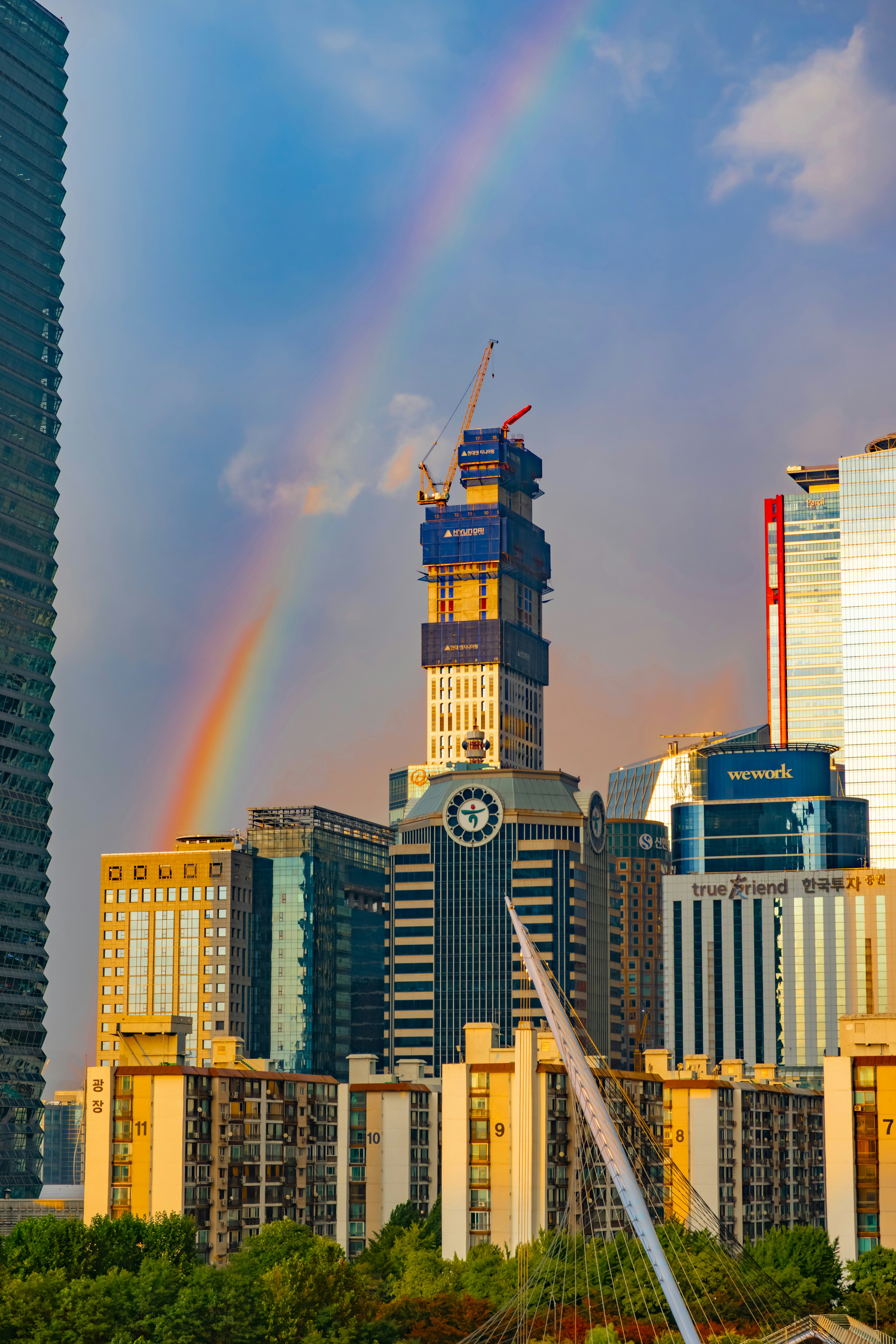 Rainbow Arc Over a Crane-Topped Skyline at Golden Hour