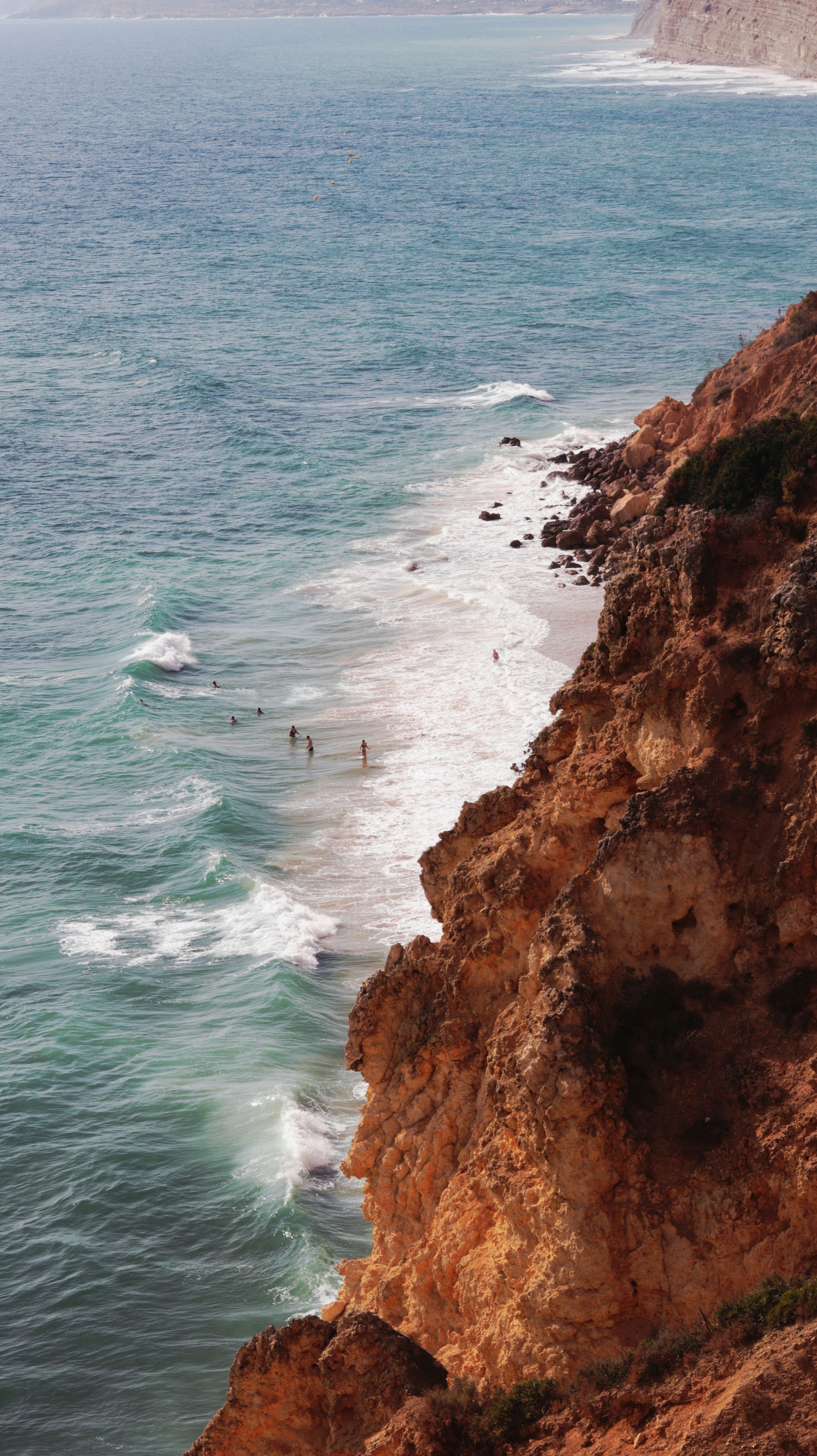 Waves gently lap against a sandy beach while people enjoy the shoreline, framed by rugged cliffs. 