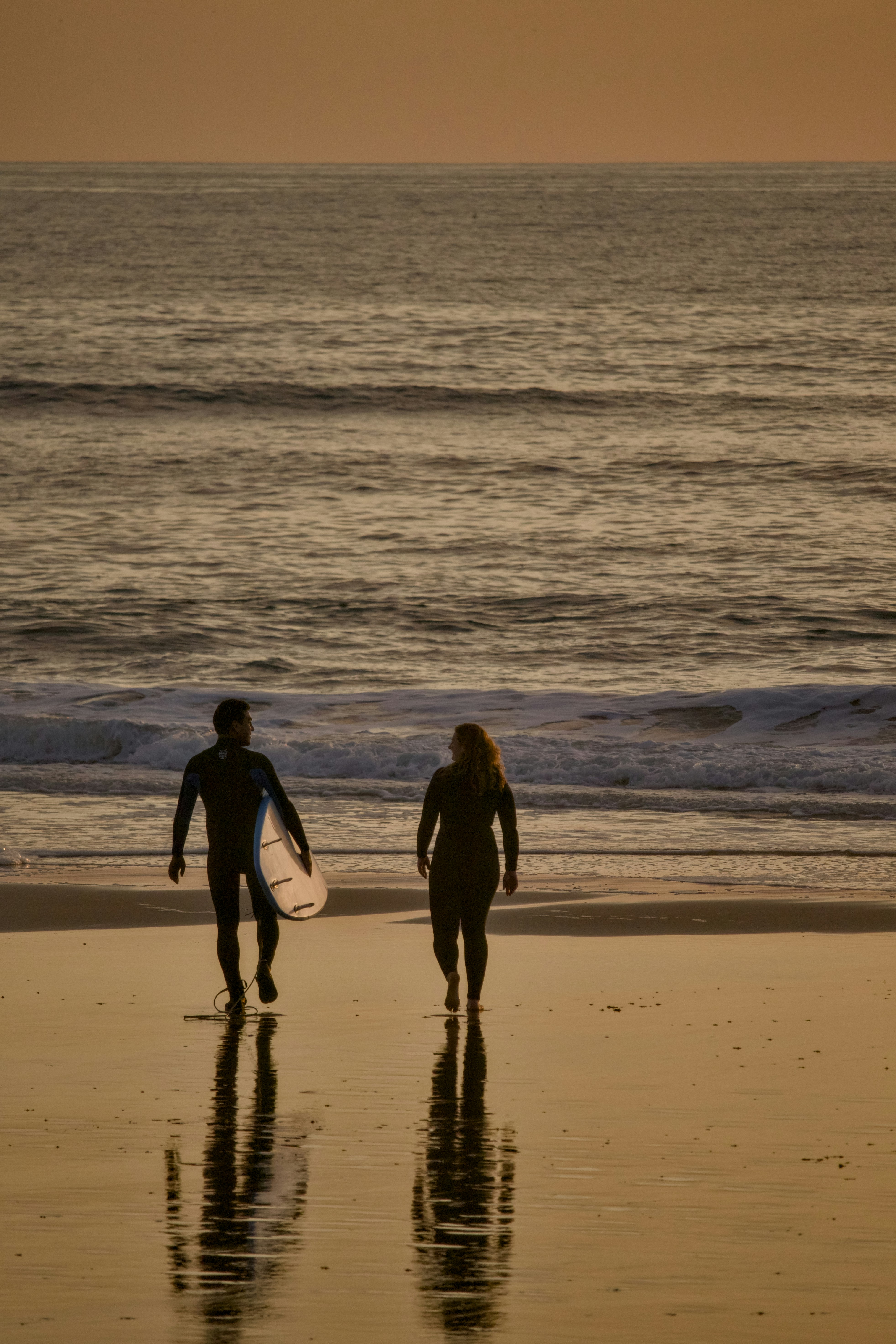Two surfers walk on beach at sunset