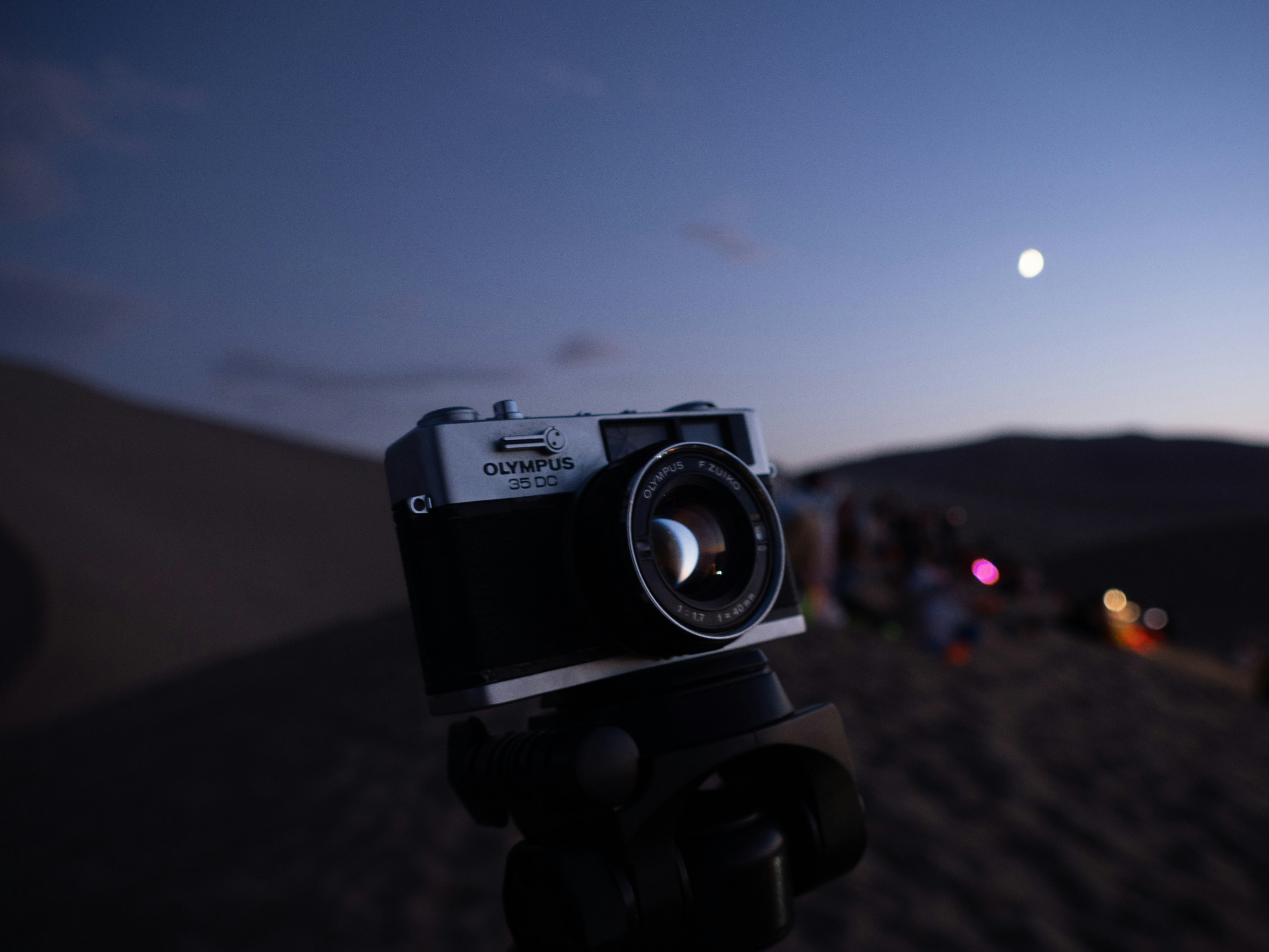 Olympus E-M1 Mark II camera positioned on a tripod against a twilight desert backdrop, with a glowing moon in the sky.