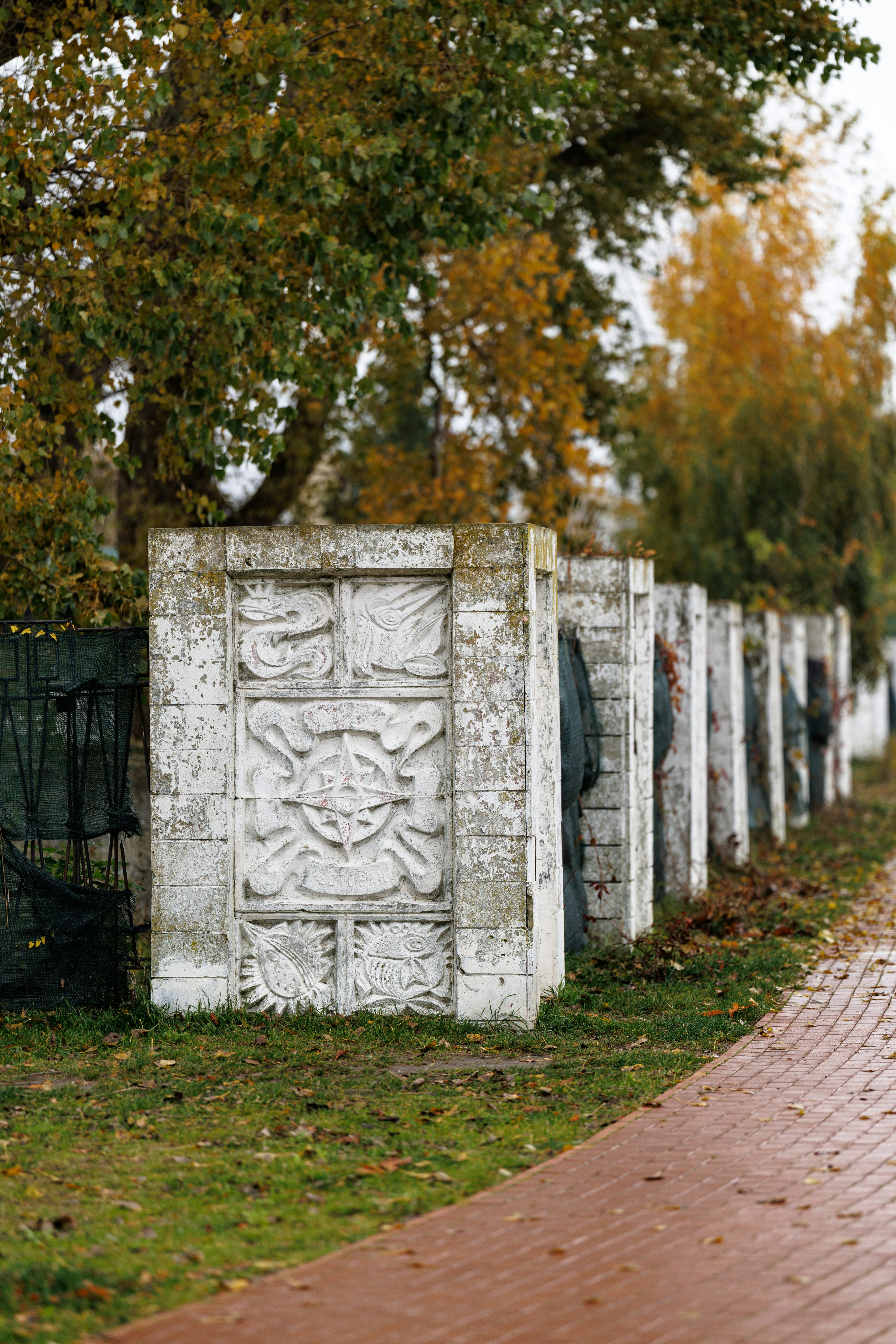 Intricately carved stone panels line a winding pathway, framed by autumn foliage, evoking a sense of history and serenity.
