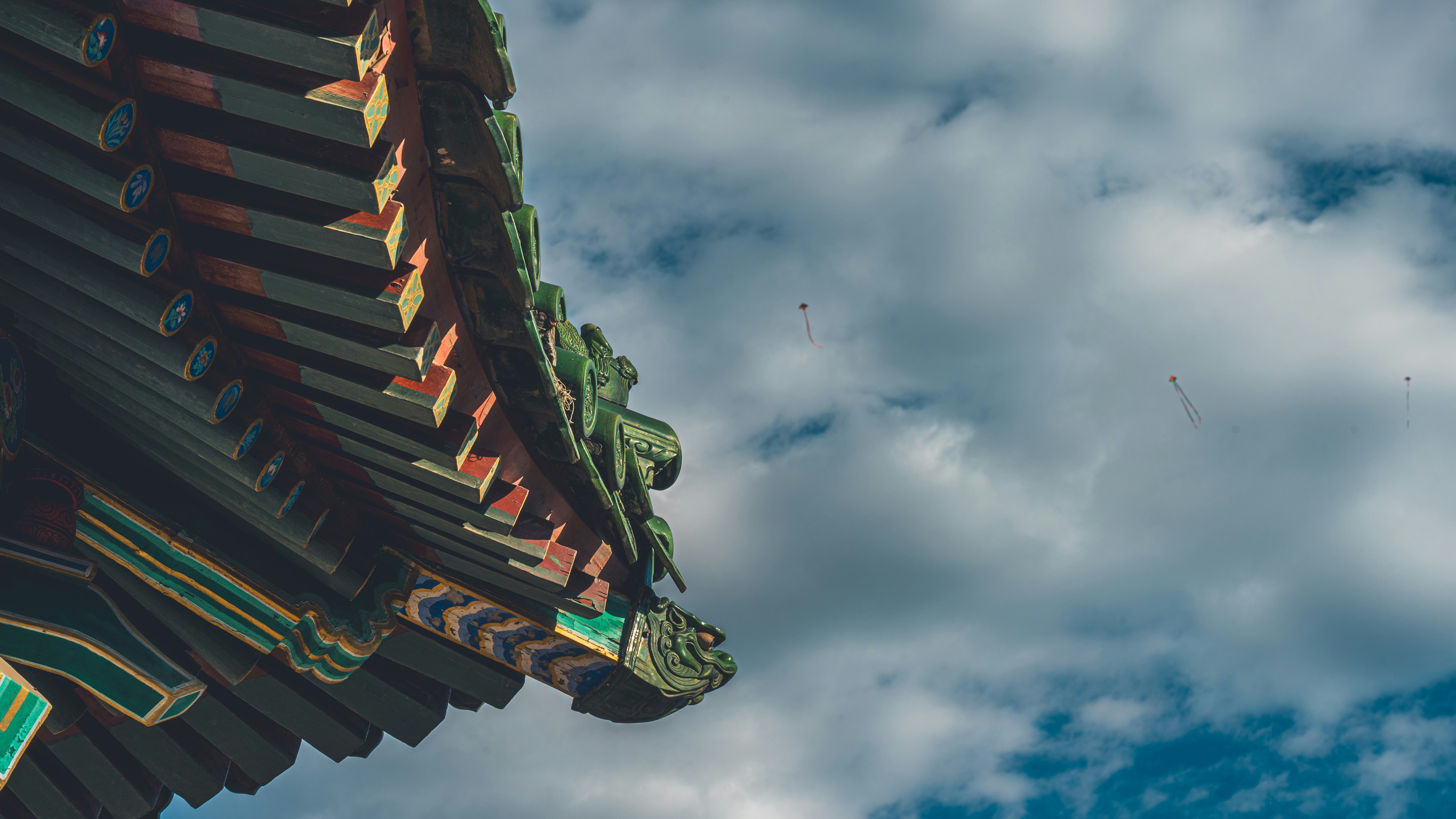 Intricate eaves of a traditional structure against a backdrop of dynamic clouds. The colorful detailing showcases cultural craftsmanship.