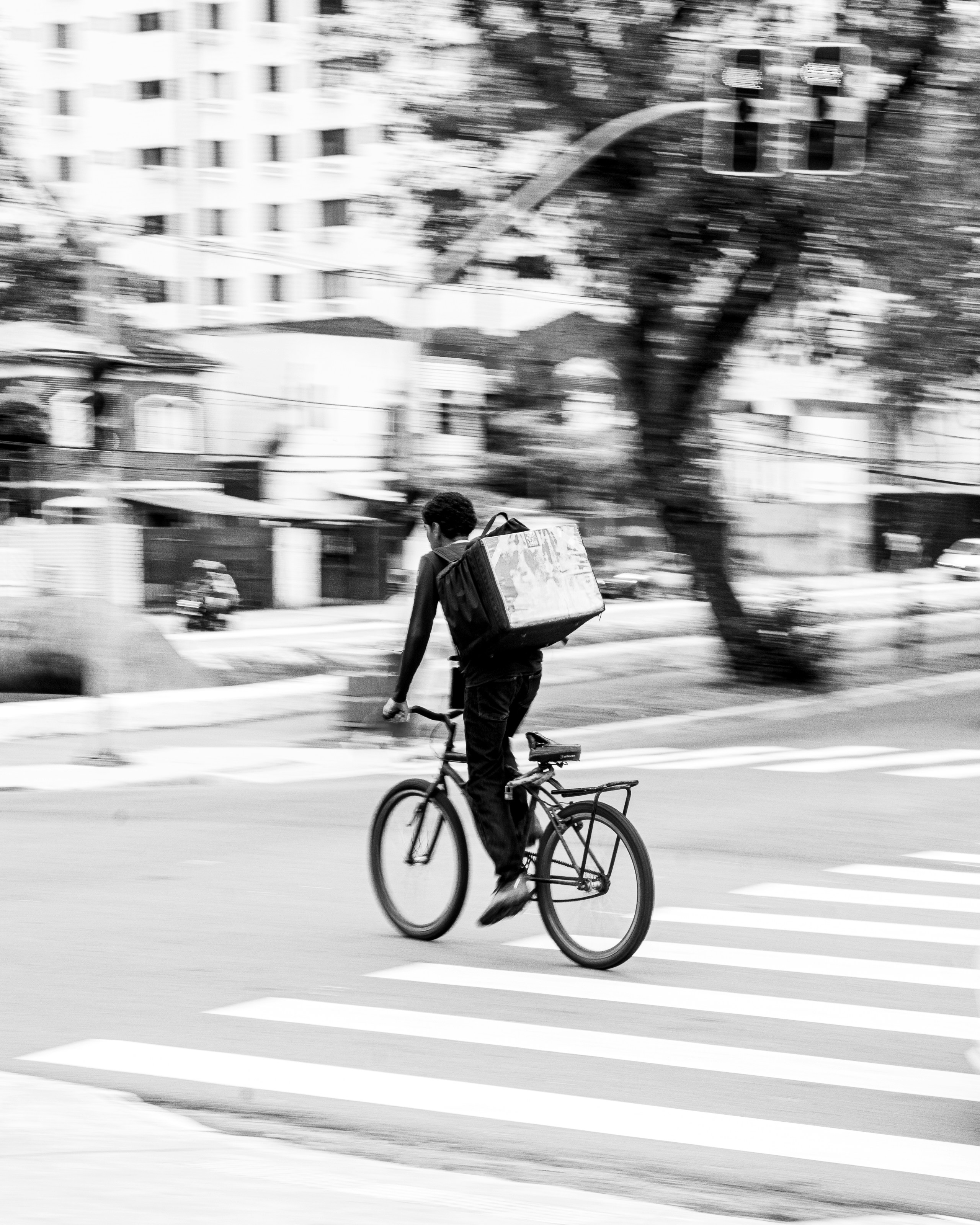 A cyclist navigates a city street, captured in motion with a blurred background conveying speed. The scene is presented in black and white, emphasizing the dynamic movement.